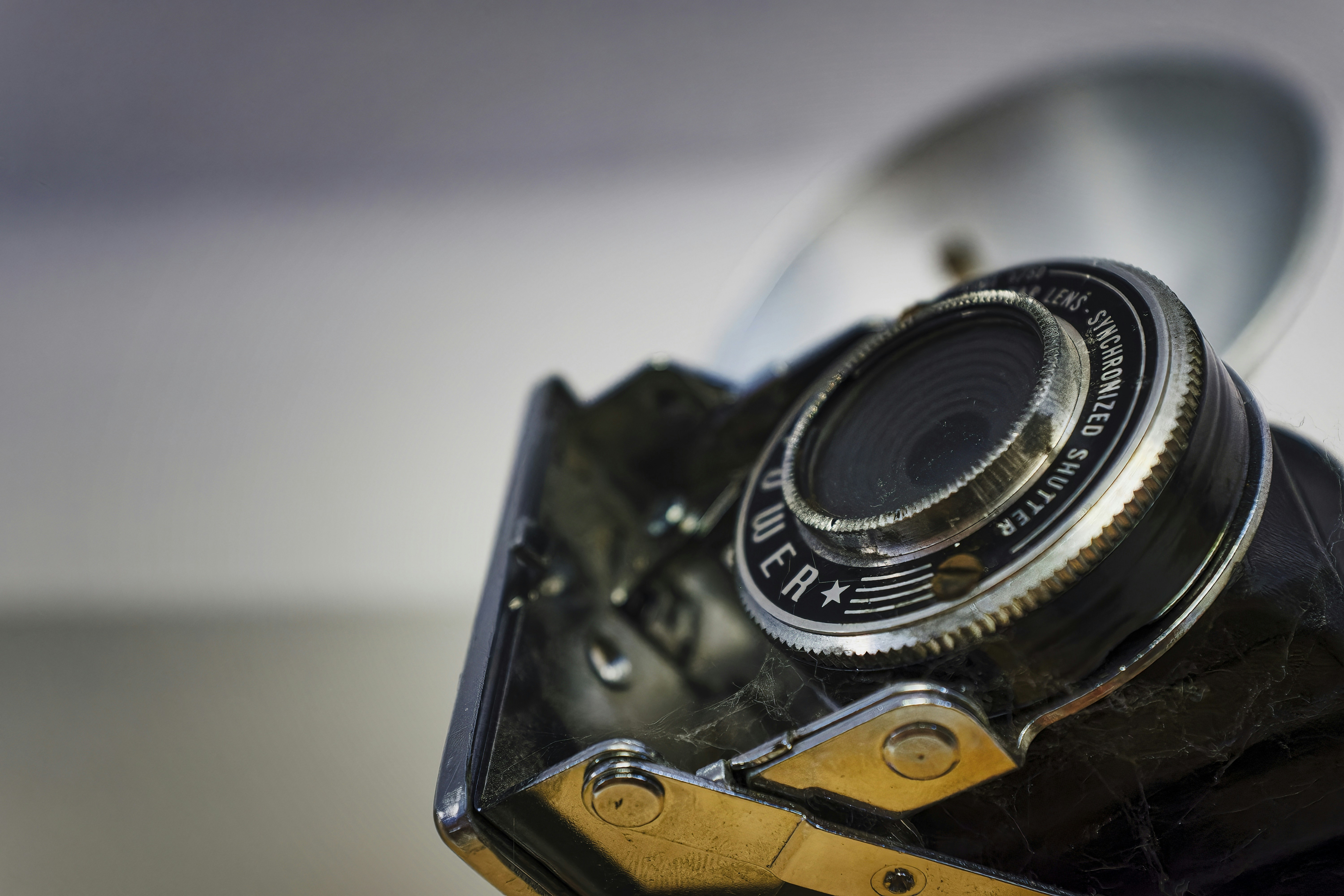 This close-up image captures the intricate details of a vintage camera lens, showcasing its metallic textures and the delicate engravings on the shutter ring. The composition focuses on the lens's circular design, set against a softly blurred background that enhances the sense of nostalgia. The lighting highlights the subtle interplay of shadows and reflections, creating a mood of timeless elegance.