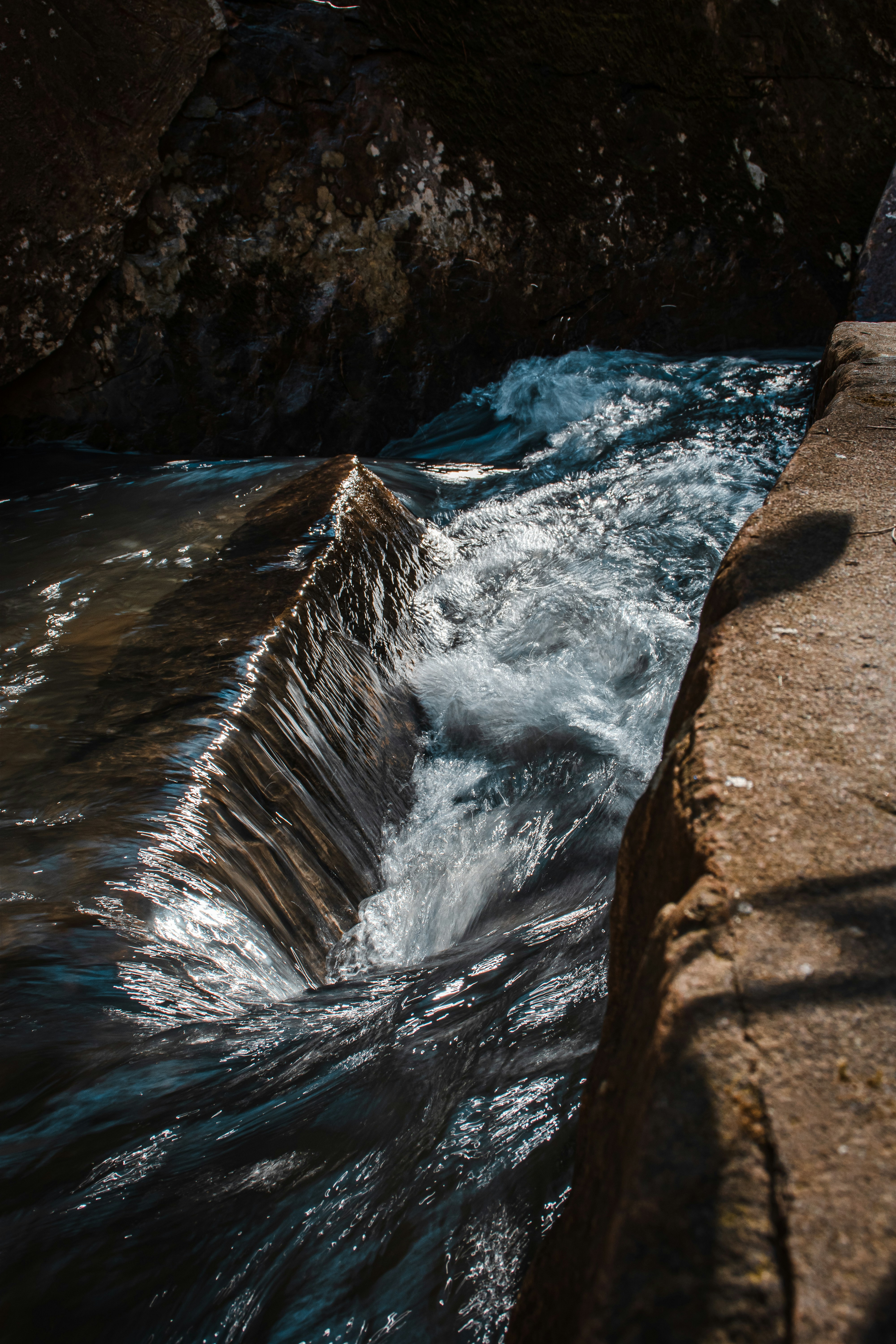 A person standing on a ledge next to a body of water photo – Free ...