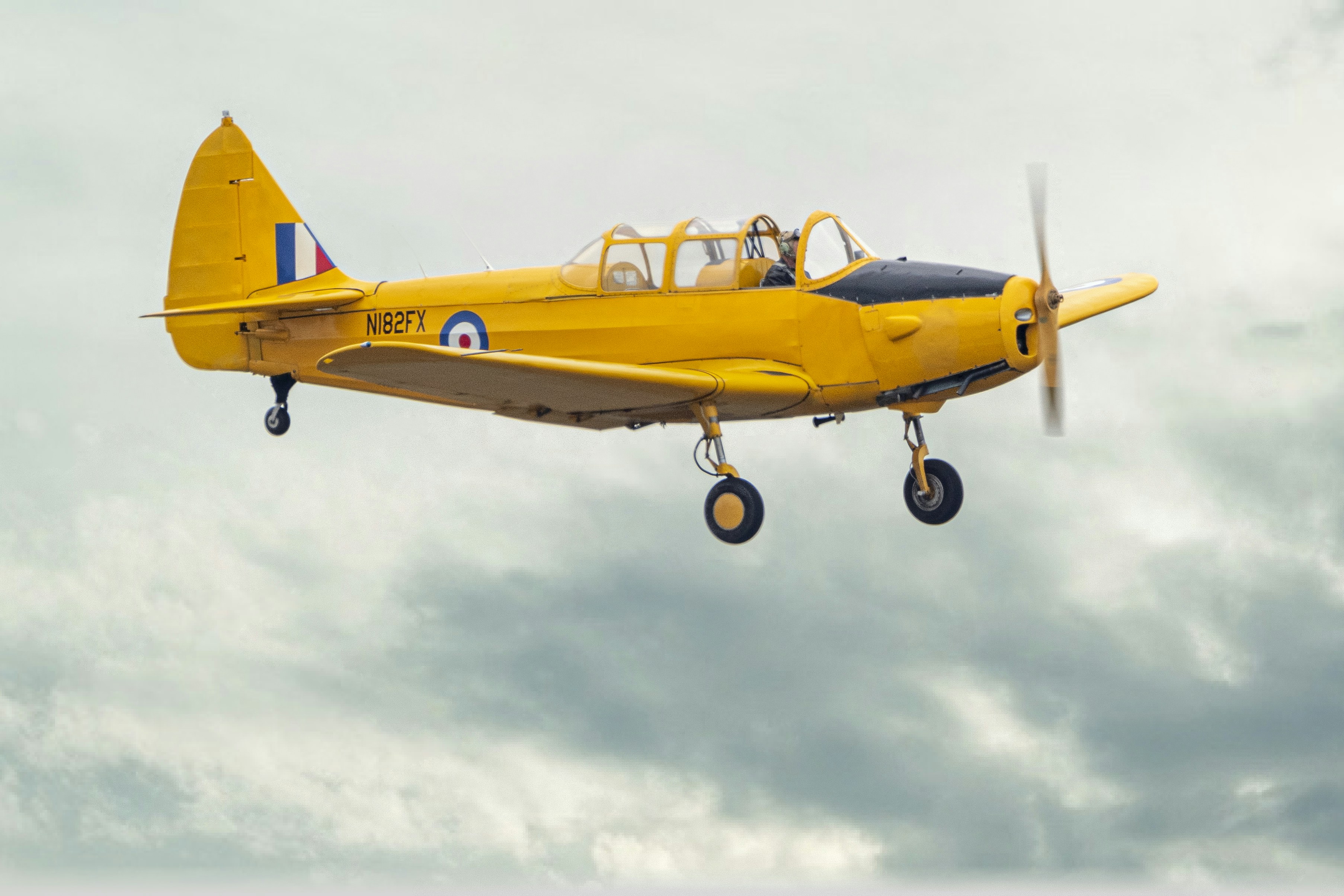 A small yellow airplane flying through a cloudy sky photo – Free Flying ...
