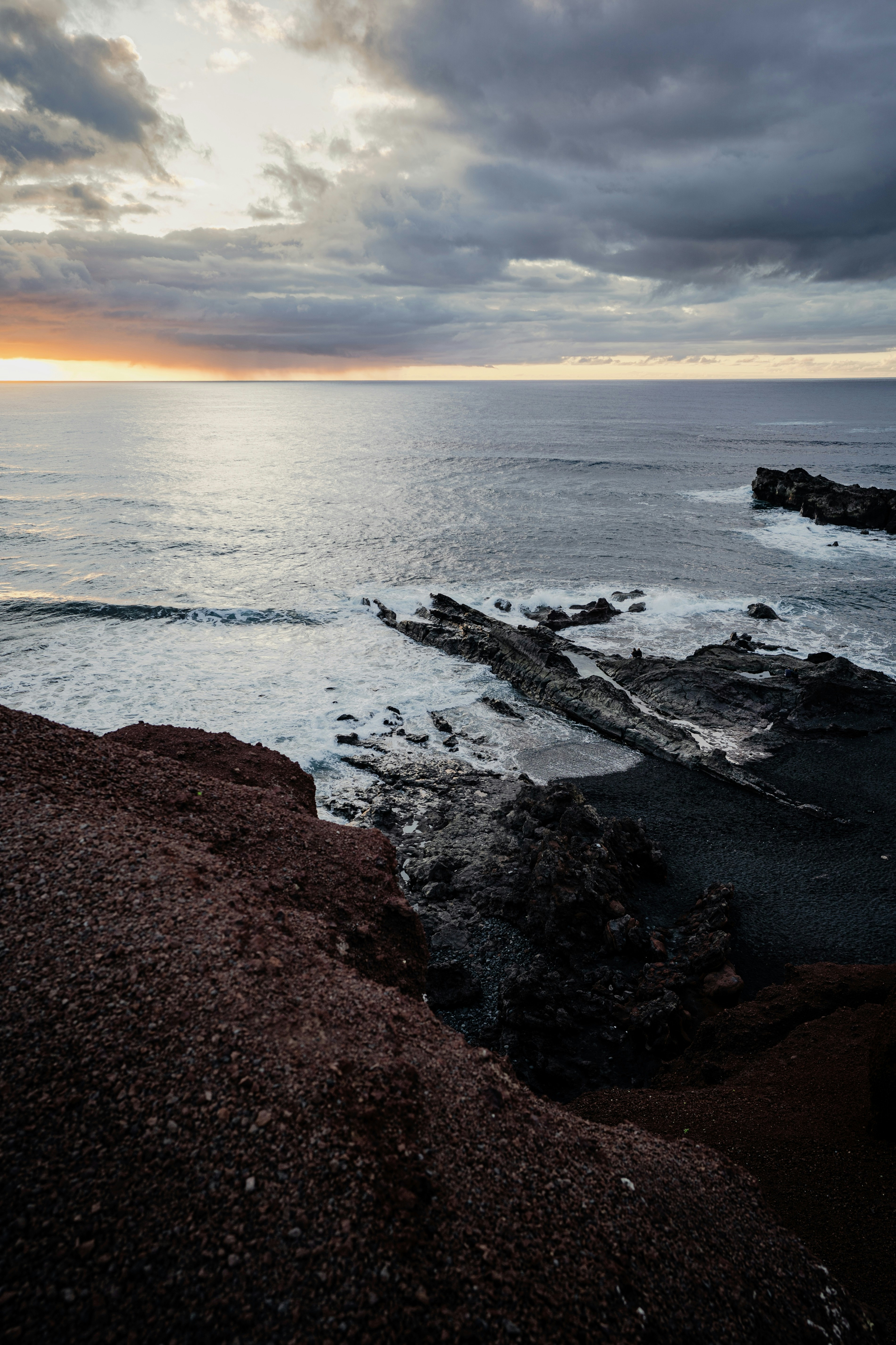 Dusk on the lava-streaked coast: fractured rocks meet a calm horizon