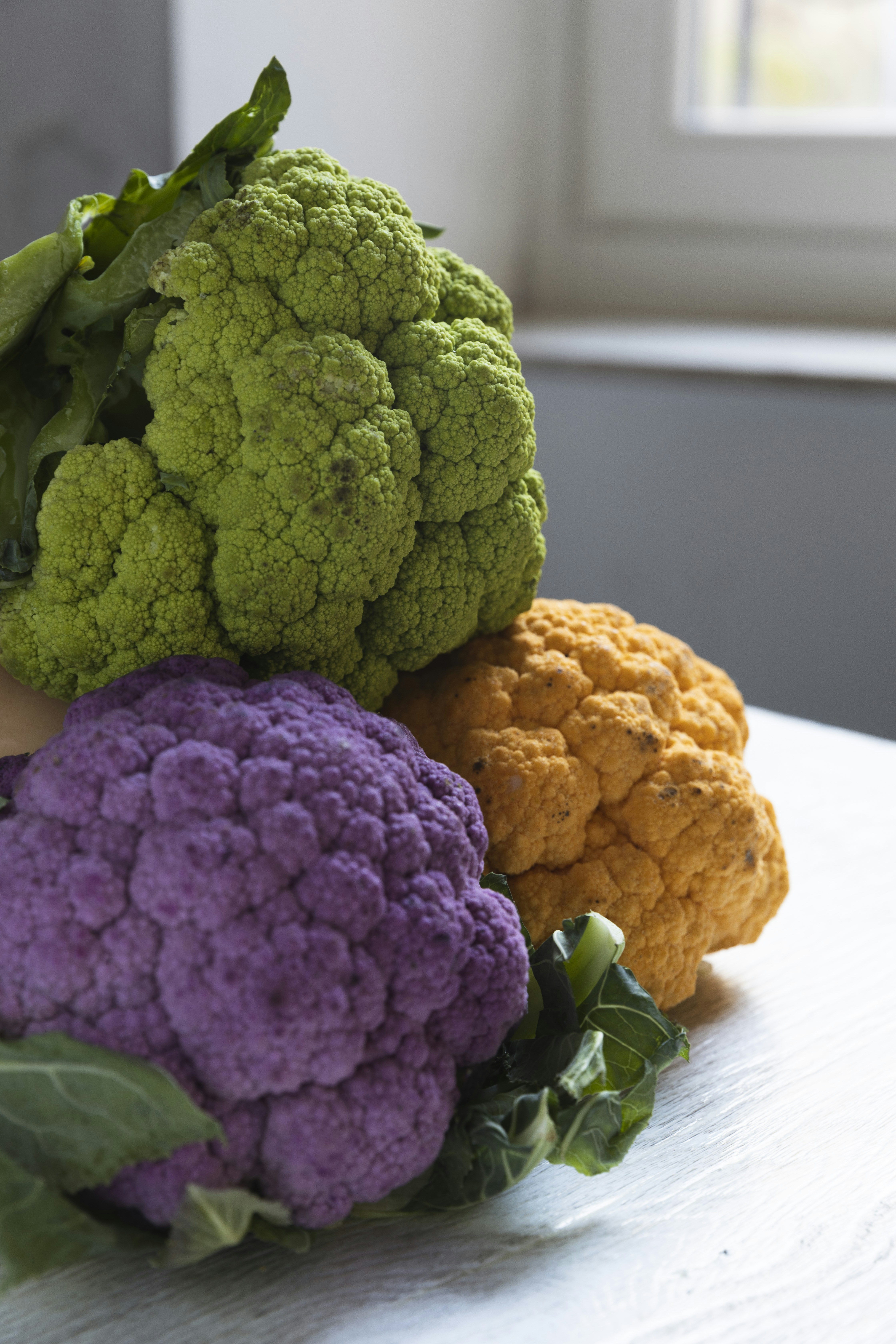 Triad of Cauliflowers: Green, Purple, and Amber resting on a sunlit tabletop