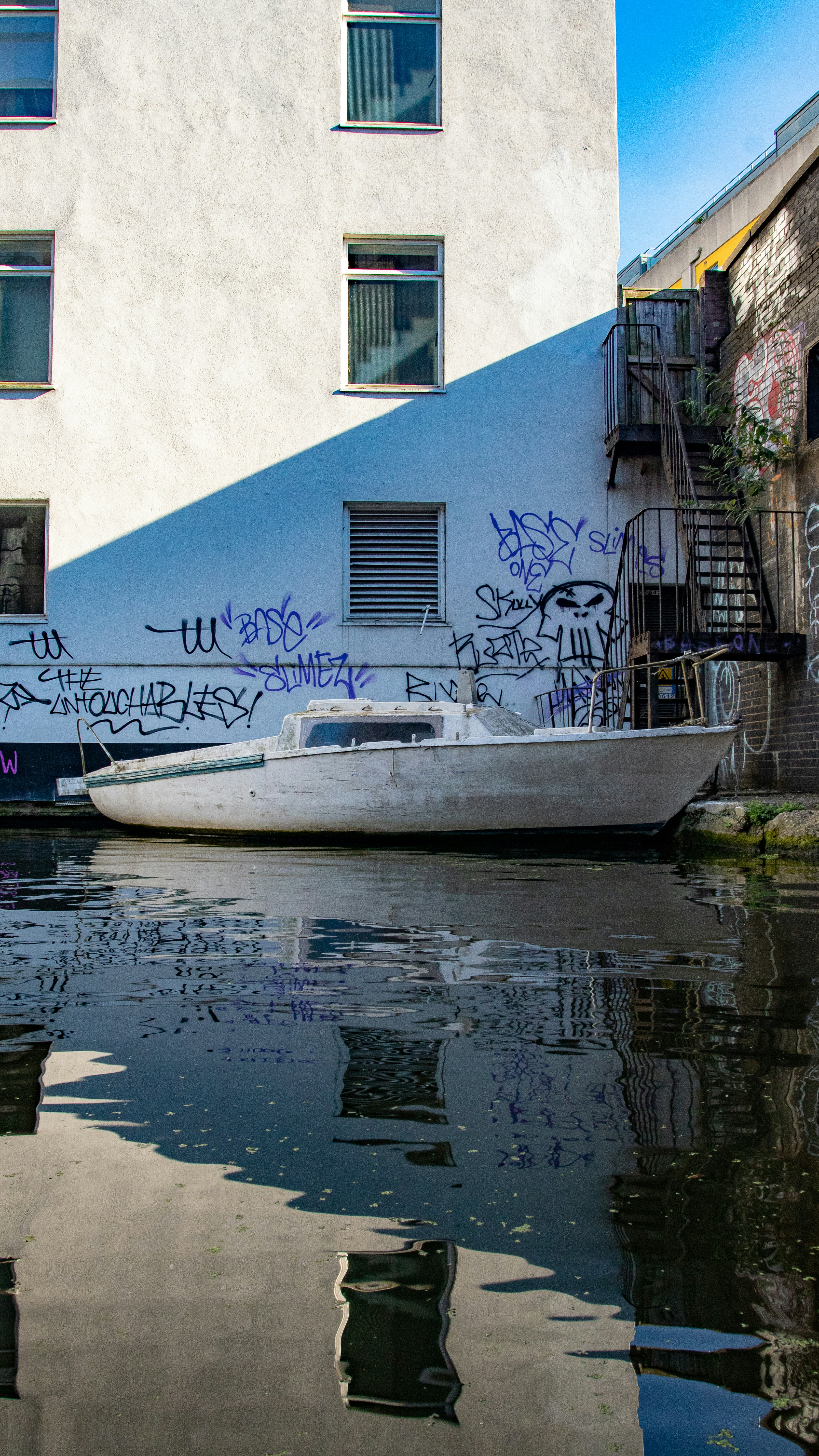 White Boat at the Graffiti Wall: Shadow and Reflection on a Calm Canal