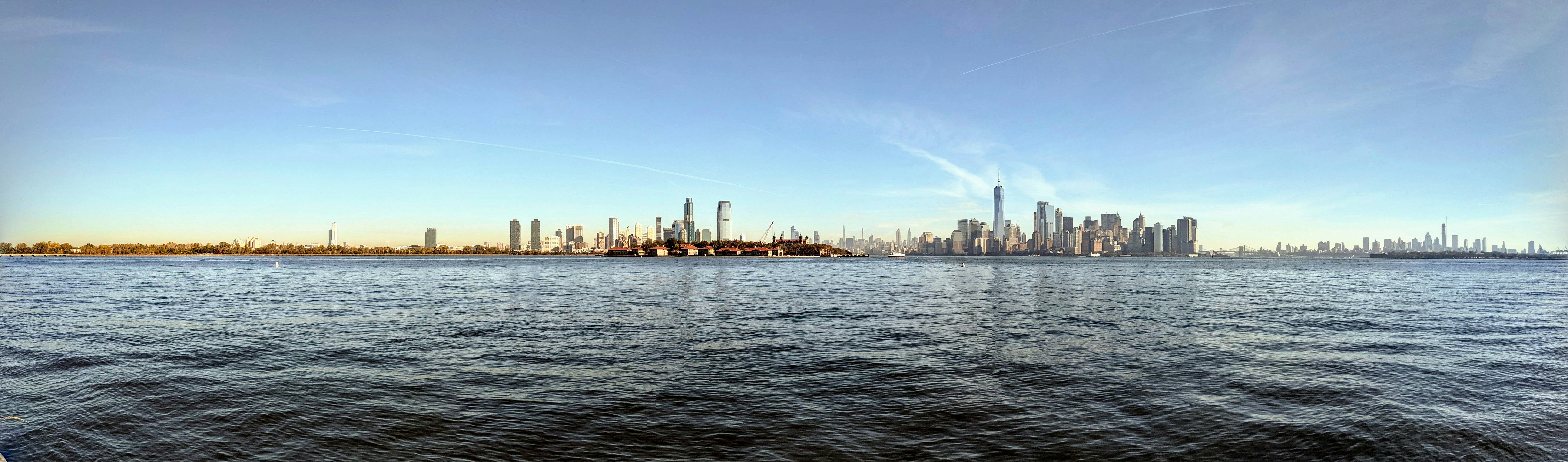 Panoramic view of a city skyline reflecting on calm waters during early morning light.