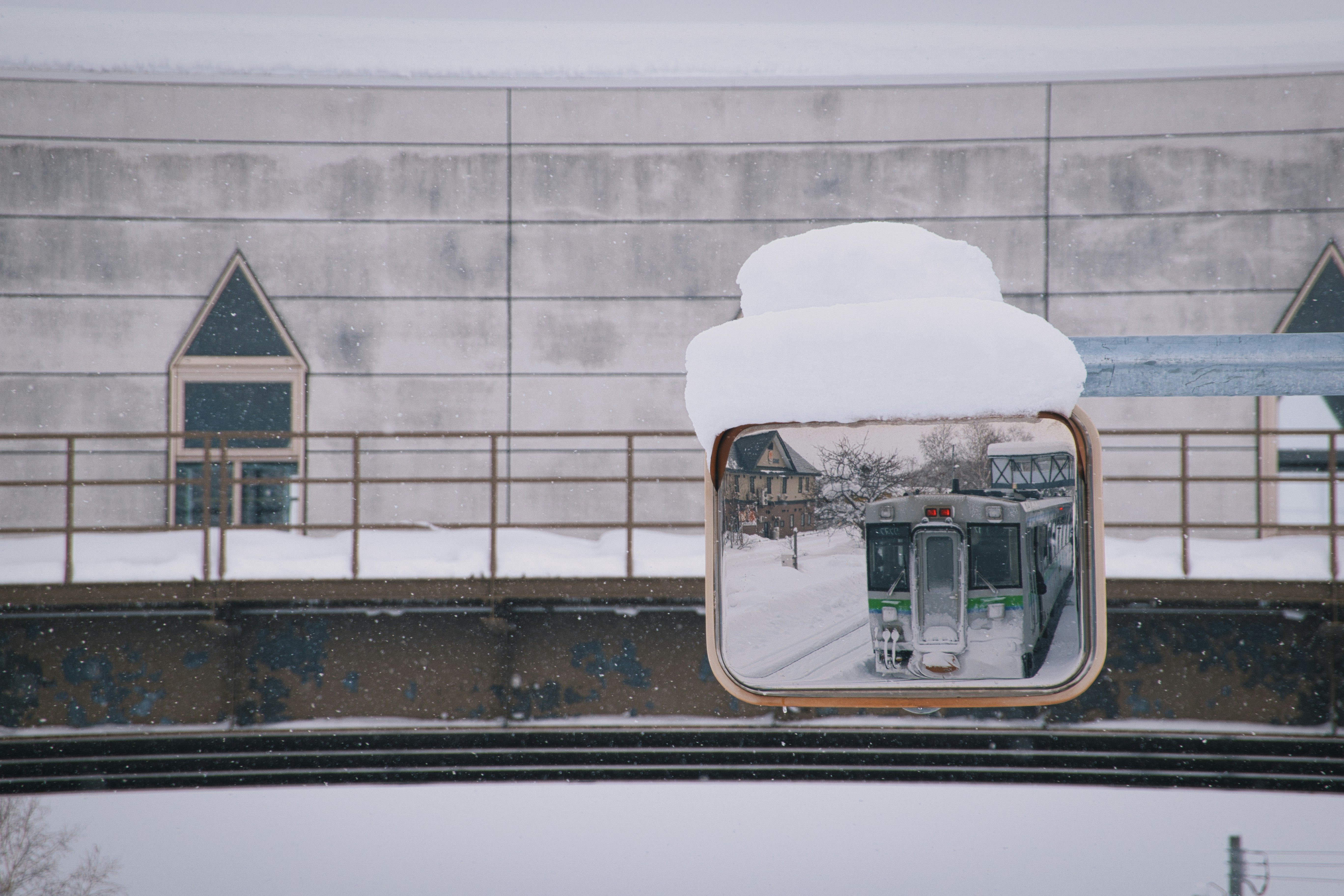 Snow-Covered Rearview Mirror Reflecting a Suburban Train