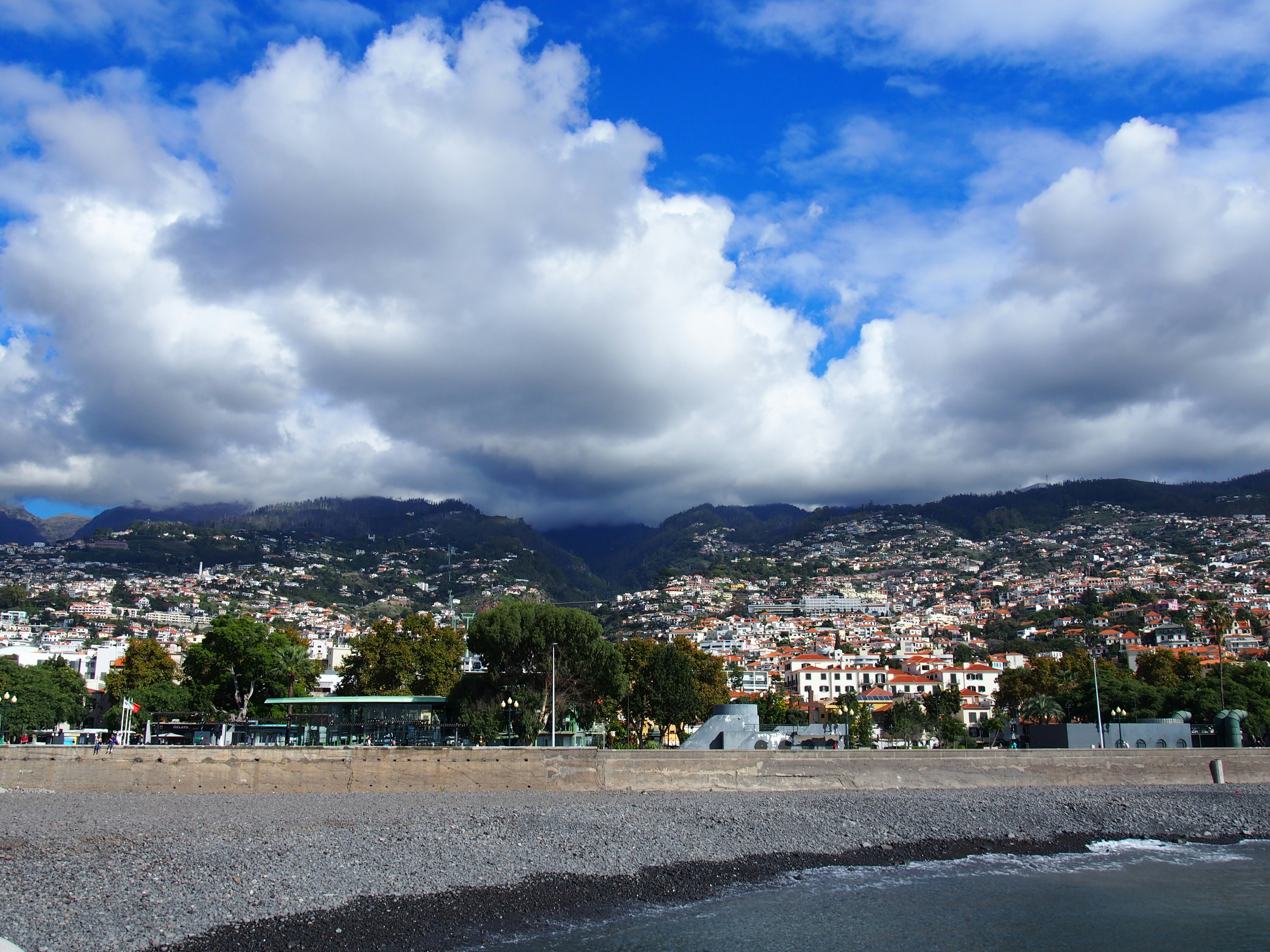 Vibrant coastal town nestled against a backdrop of rolling mountains and dramatic clouds, showcasing the harmony between nature and urban life.