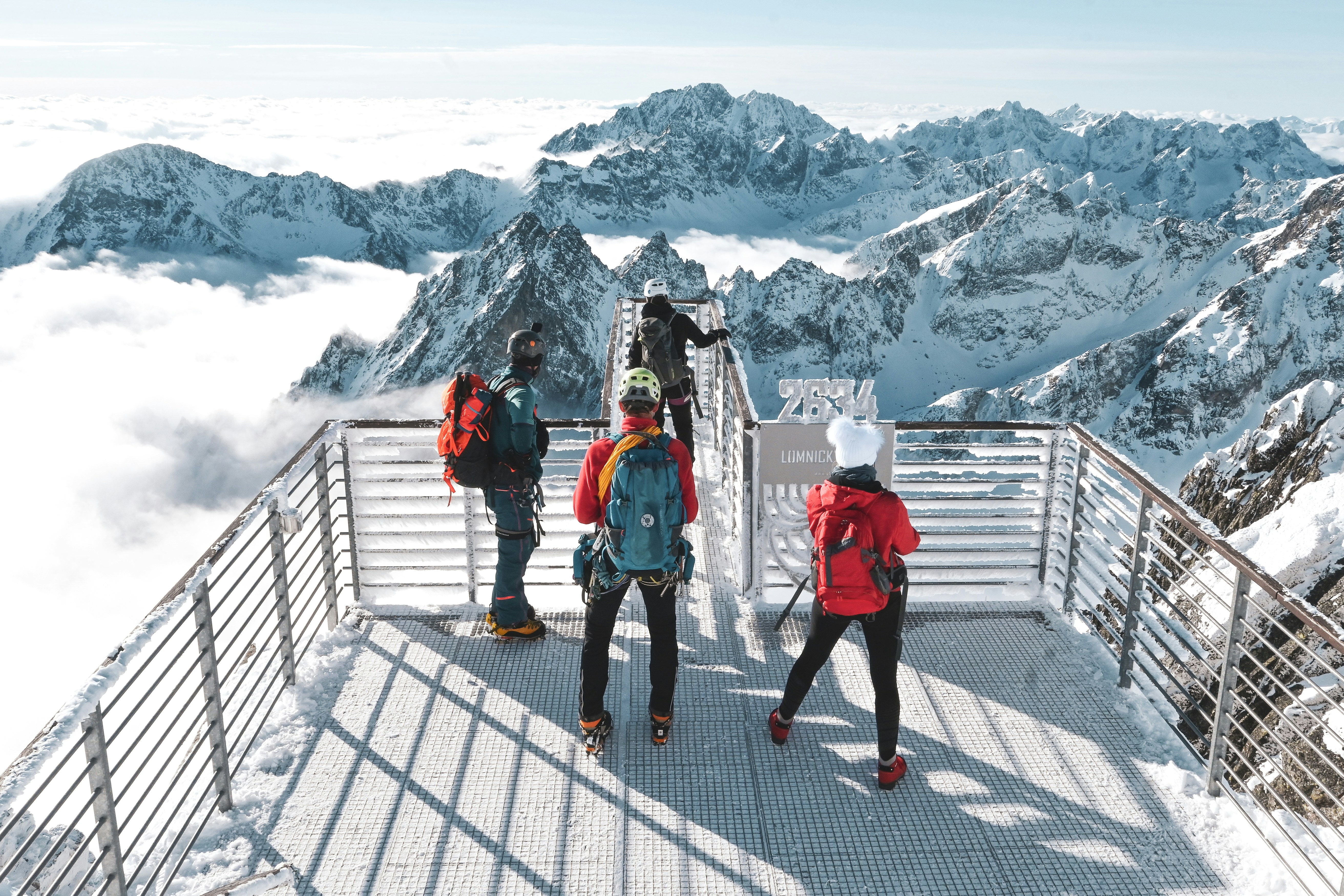 Skydeck Convergence: Four Climbers on a Snowbound Rim Above Clouds