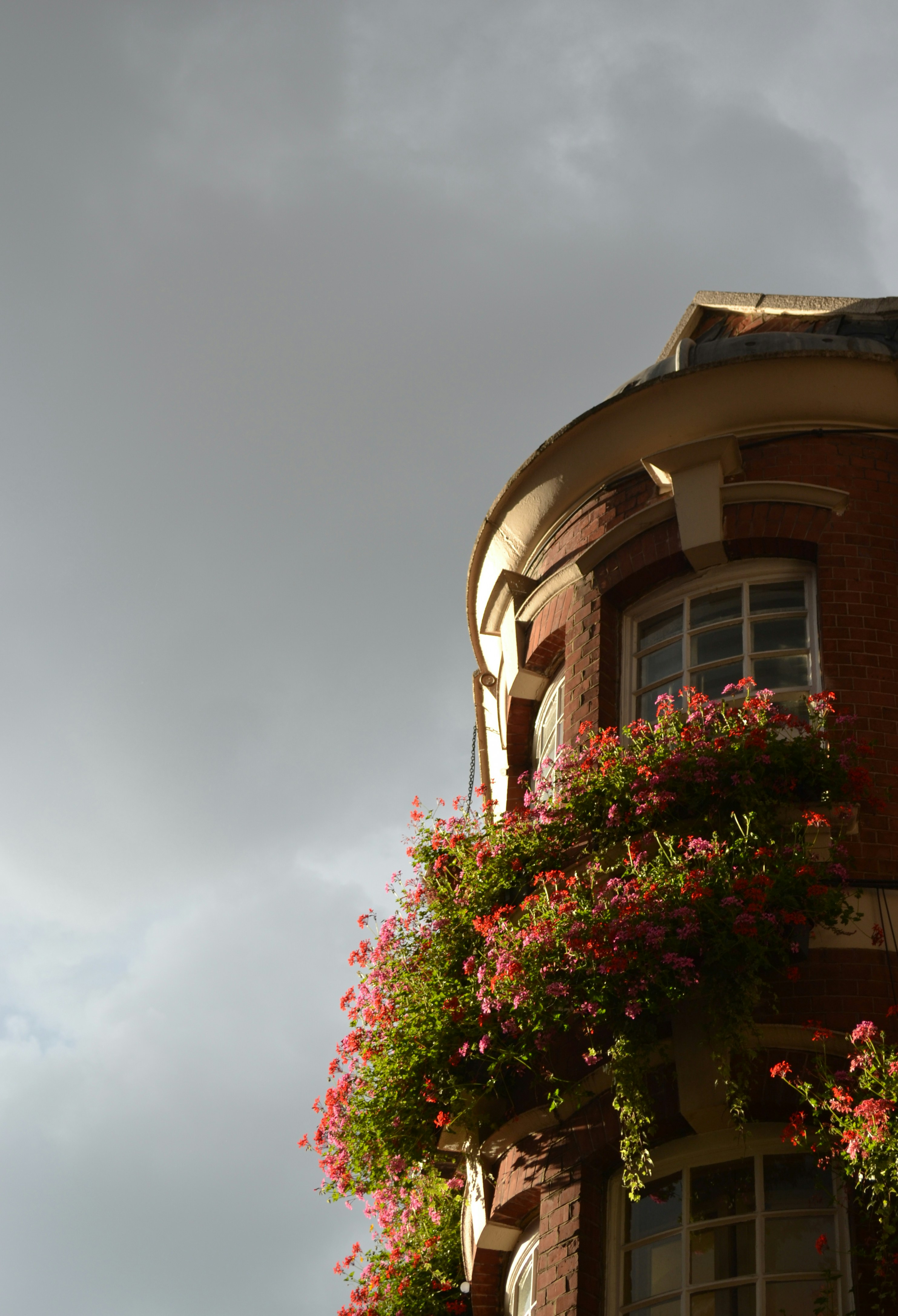 Crimson Veranda: Flowers Climbing a Brick Turret Beneath an Overcast Sky