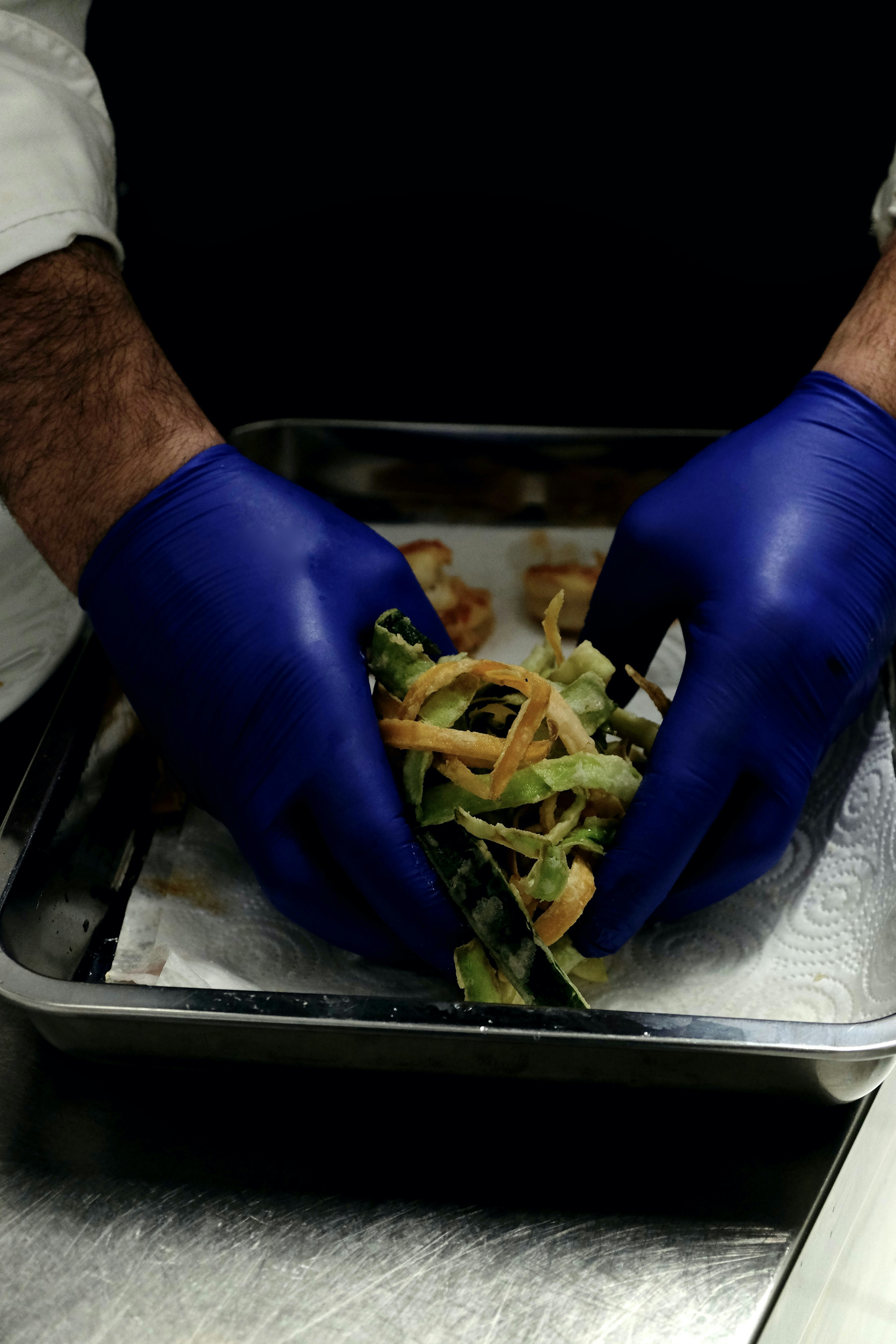 Gloved Hands Tossing Crunchy Veggie Toppers into a Tray