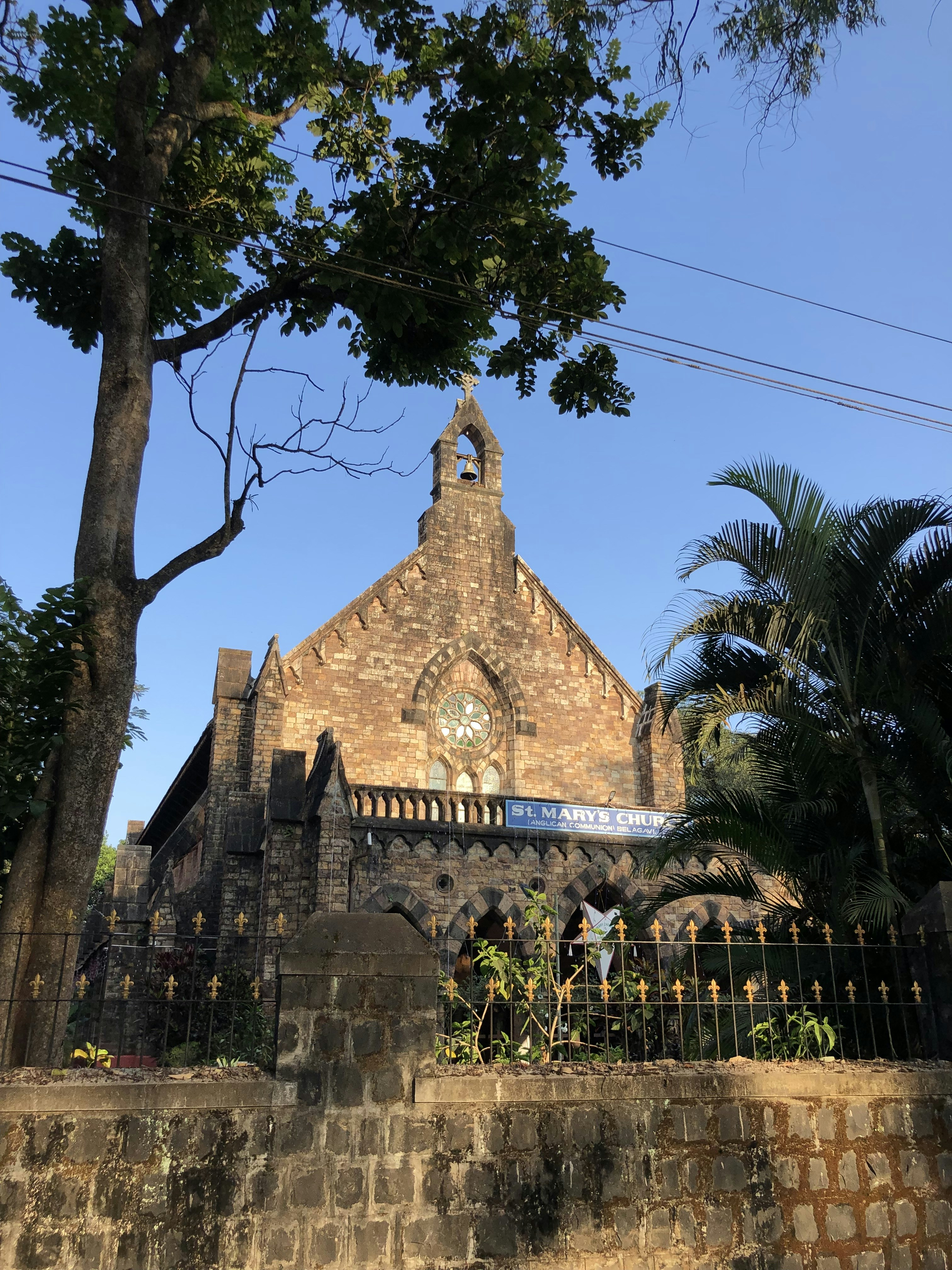Stone church with a bell tower framed by trees under a clear blue sky.