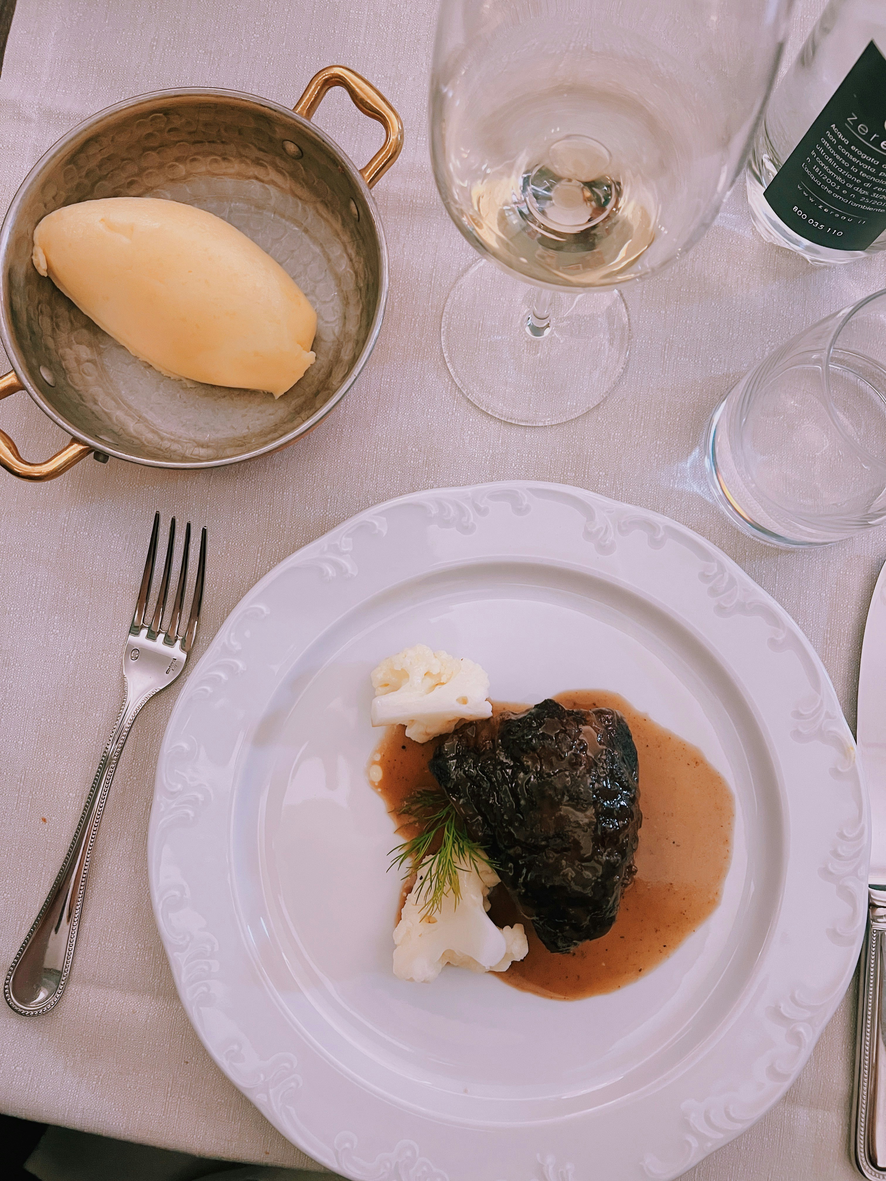 Gourmet plated dish with sauce, beurre blanc accents and a potato boat לצד a glass of white wine