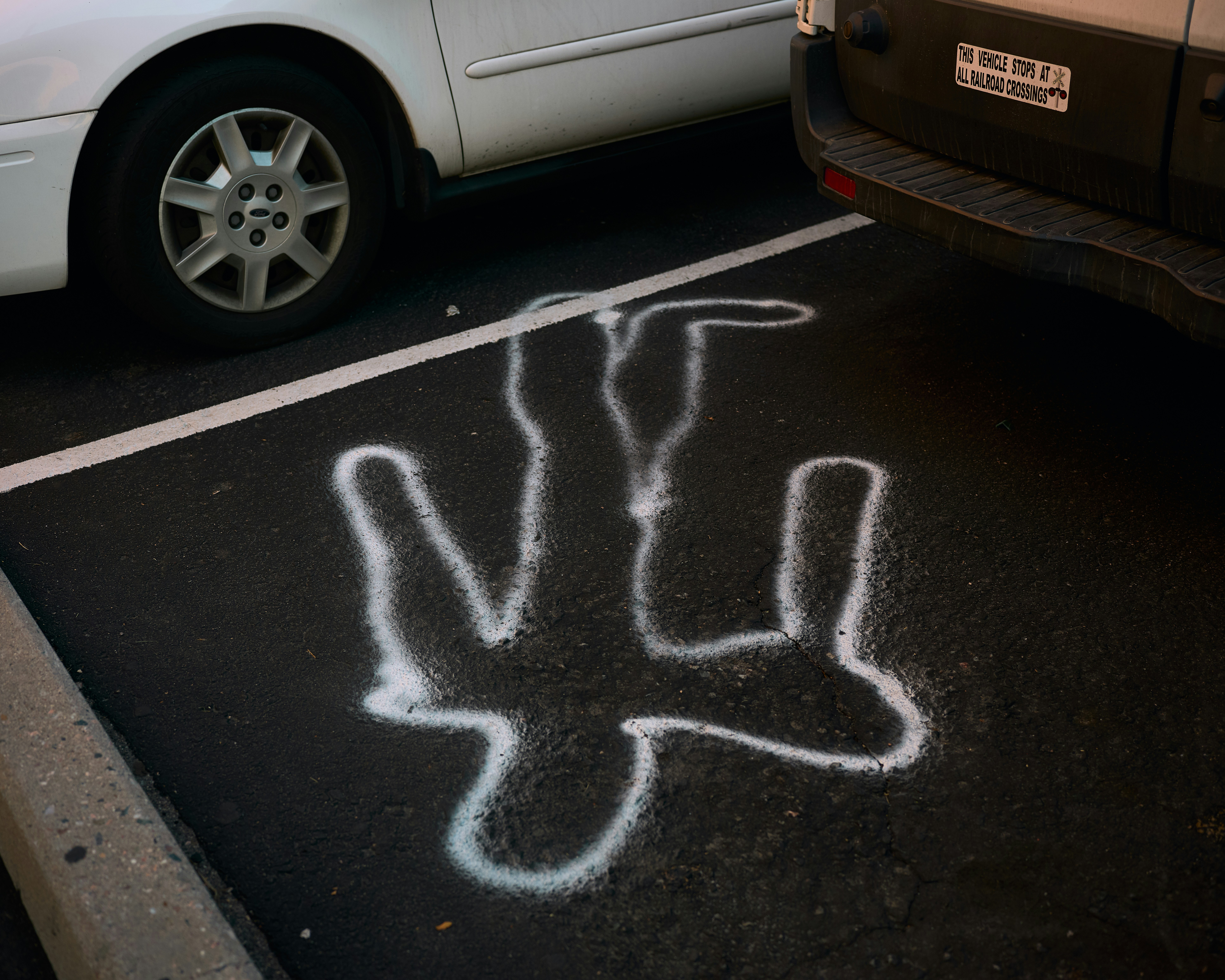 Chalk Glyph on a Rain-Damp Parking Lot Between Parked Cars