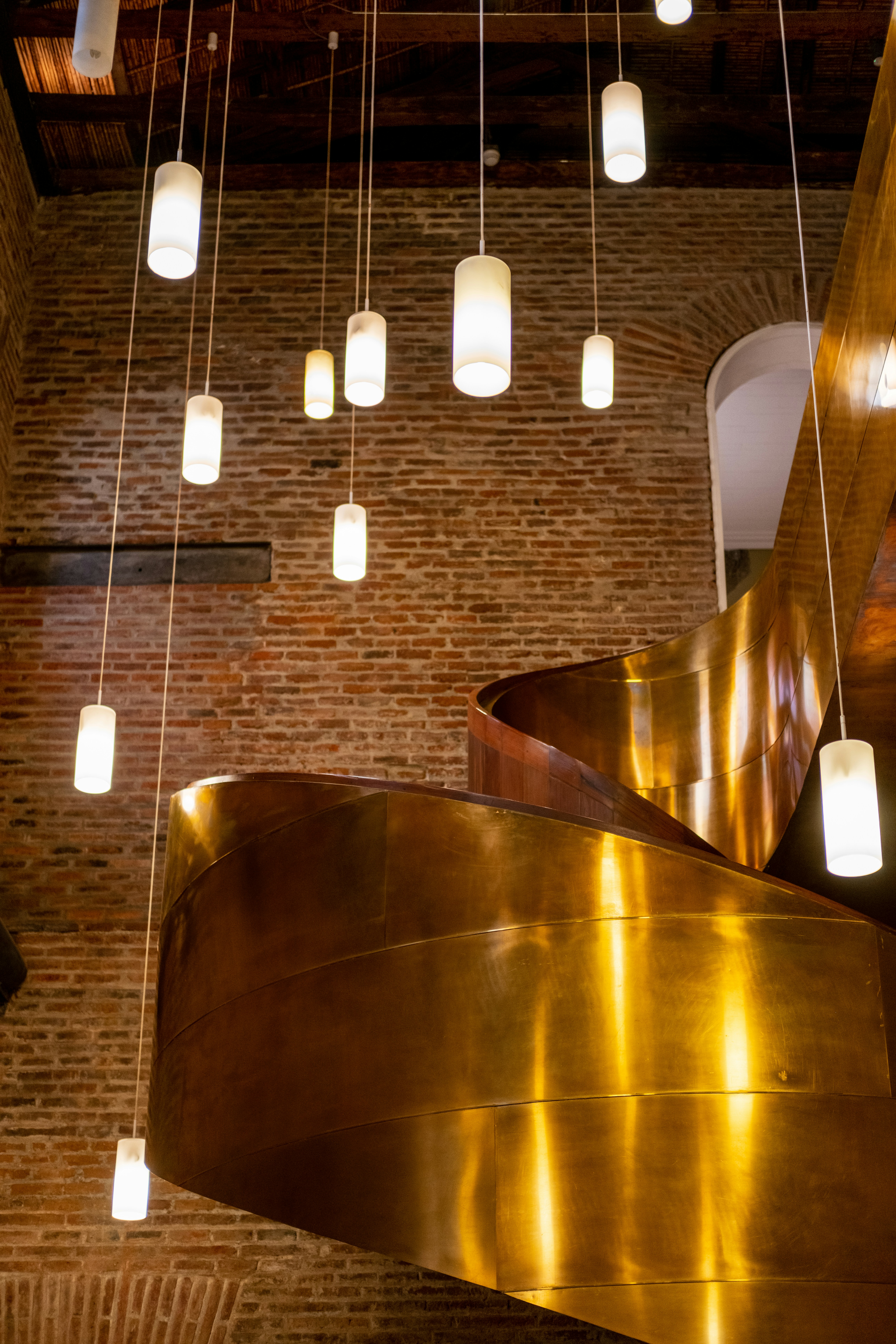 Copper Spiral Staircase Amid Hanging Lights in a Brick Atrium