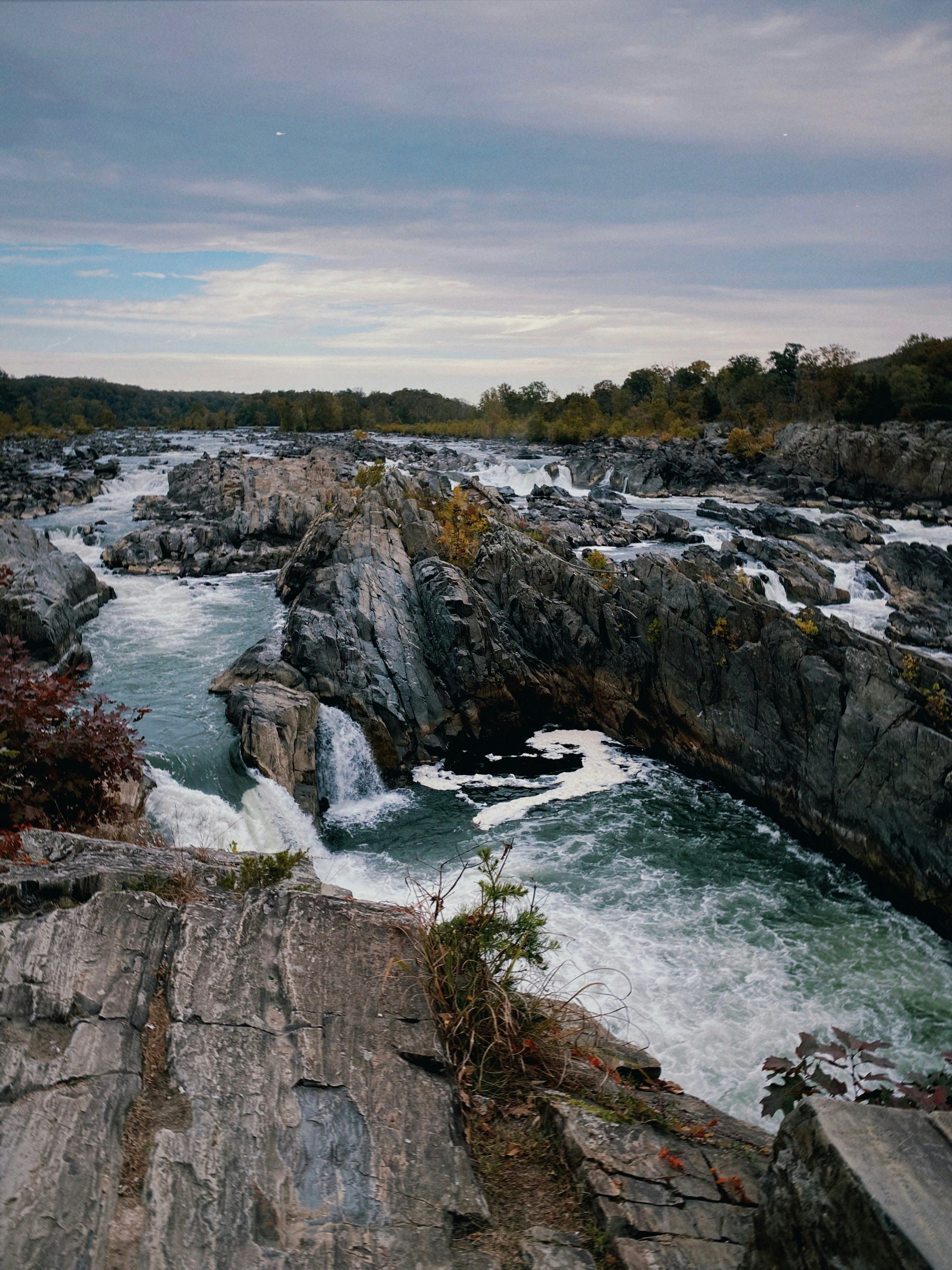 Rugged riverbanks adorned with autumn foliage, cascading waters create a serene landscape at twilight.