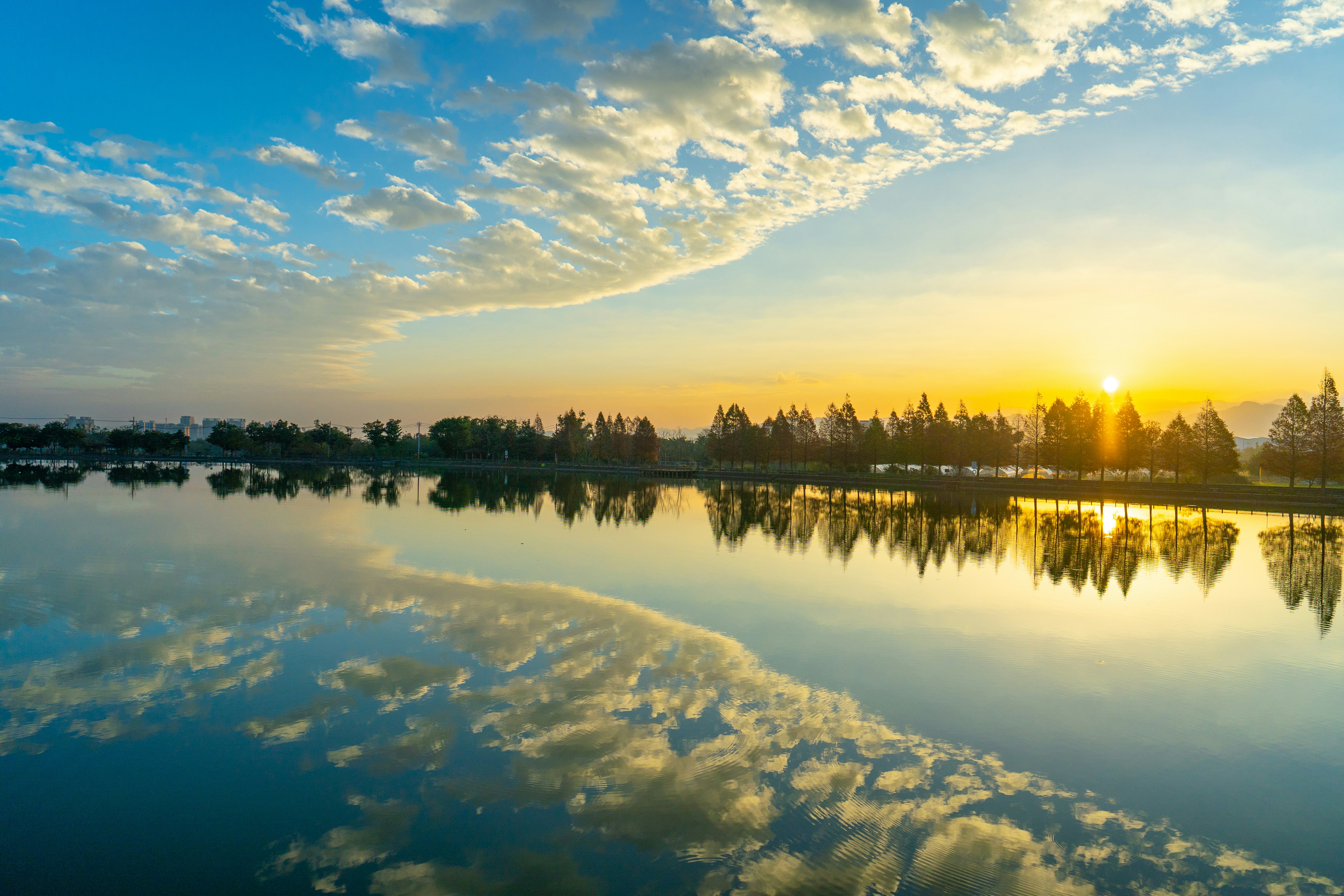 Golden sunrise reflecting on a tranquil lake with scattered clouds overhead.