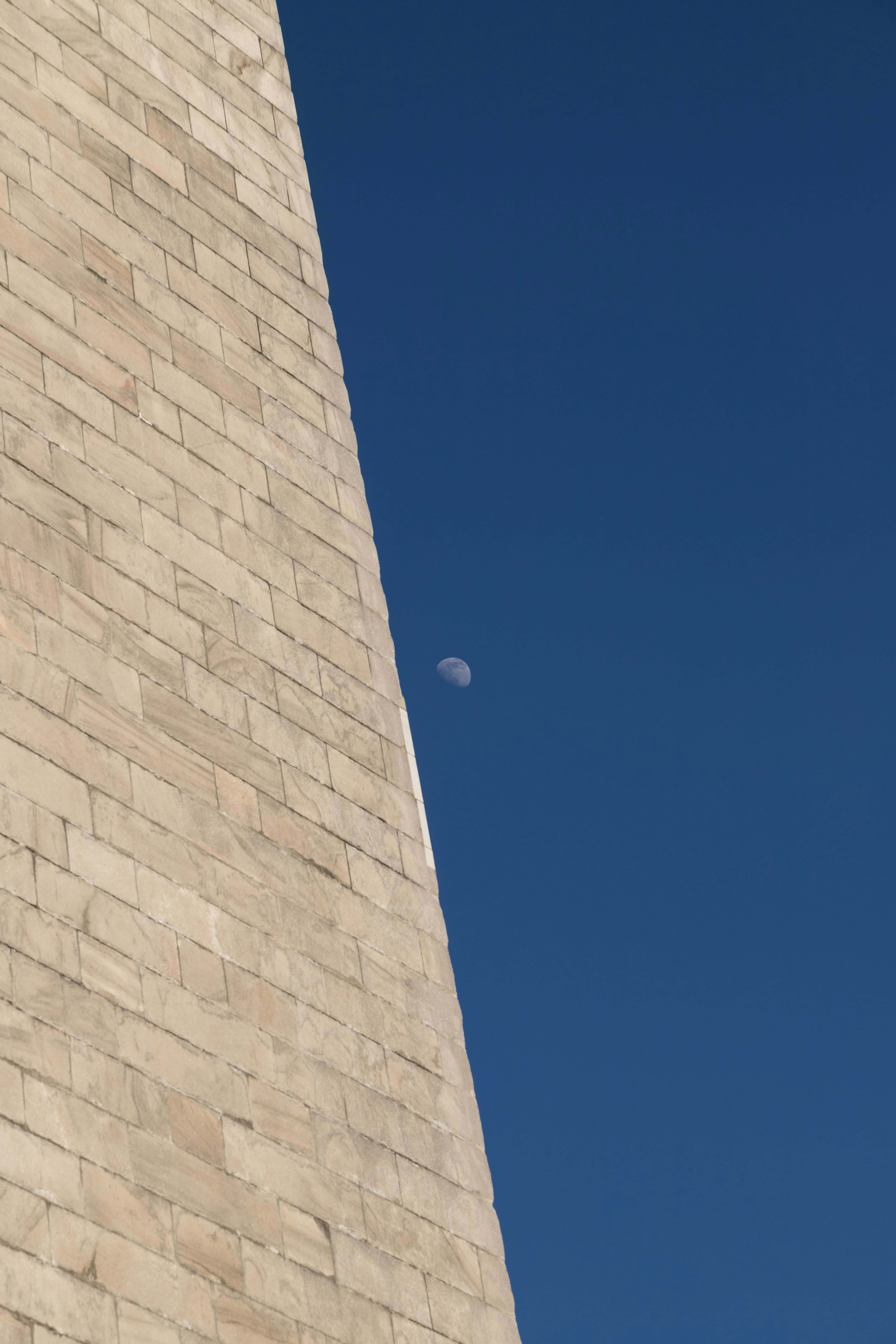 Moon over a sharply angled stone wall under a deep blue sky