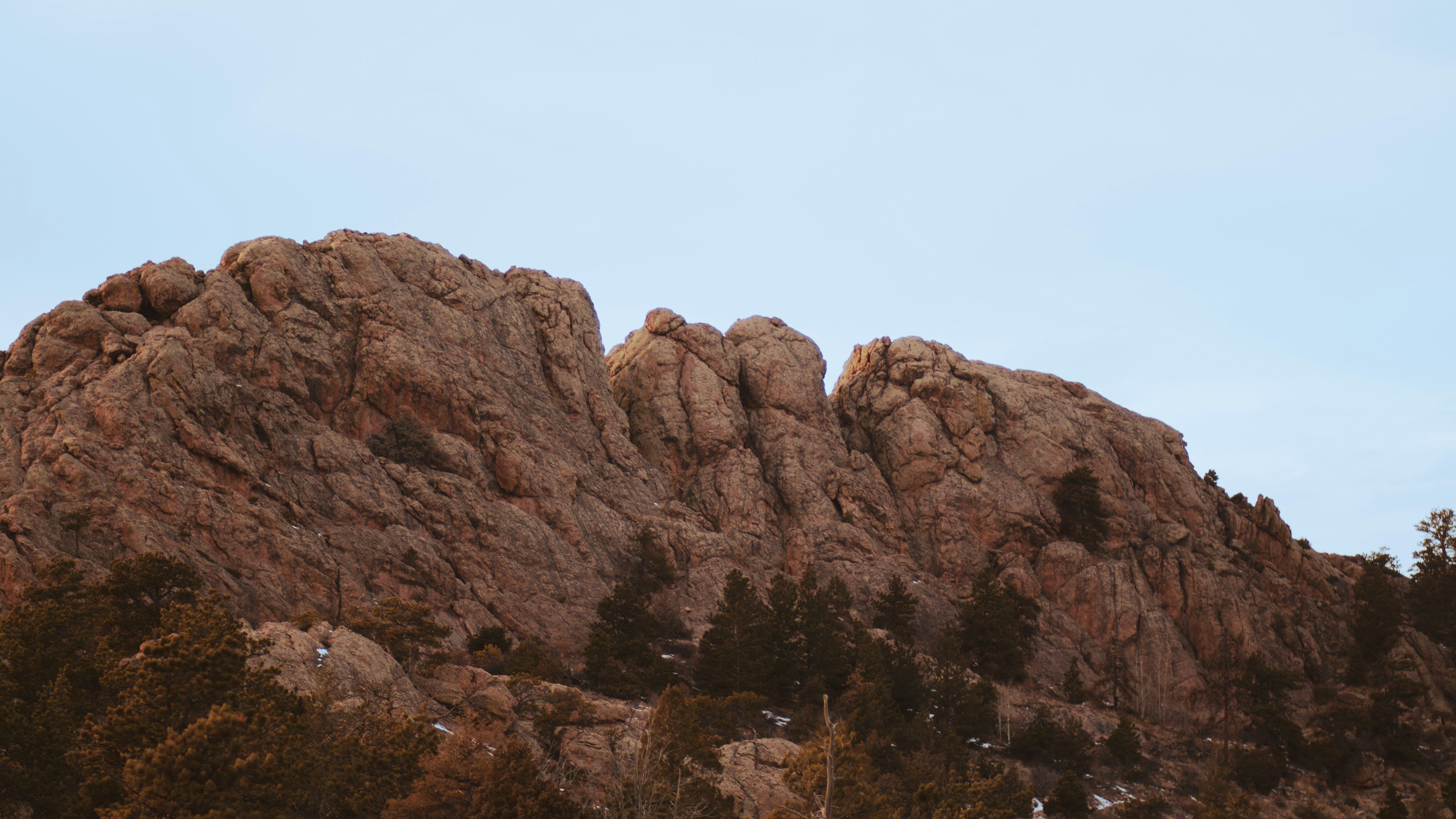 Rocky formation with scattered trees under a pastel evening sky.