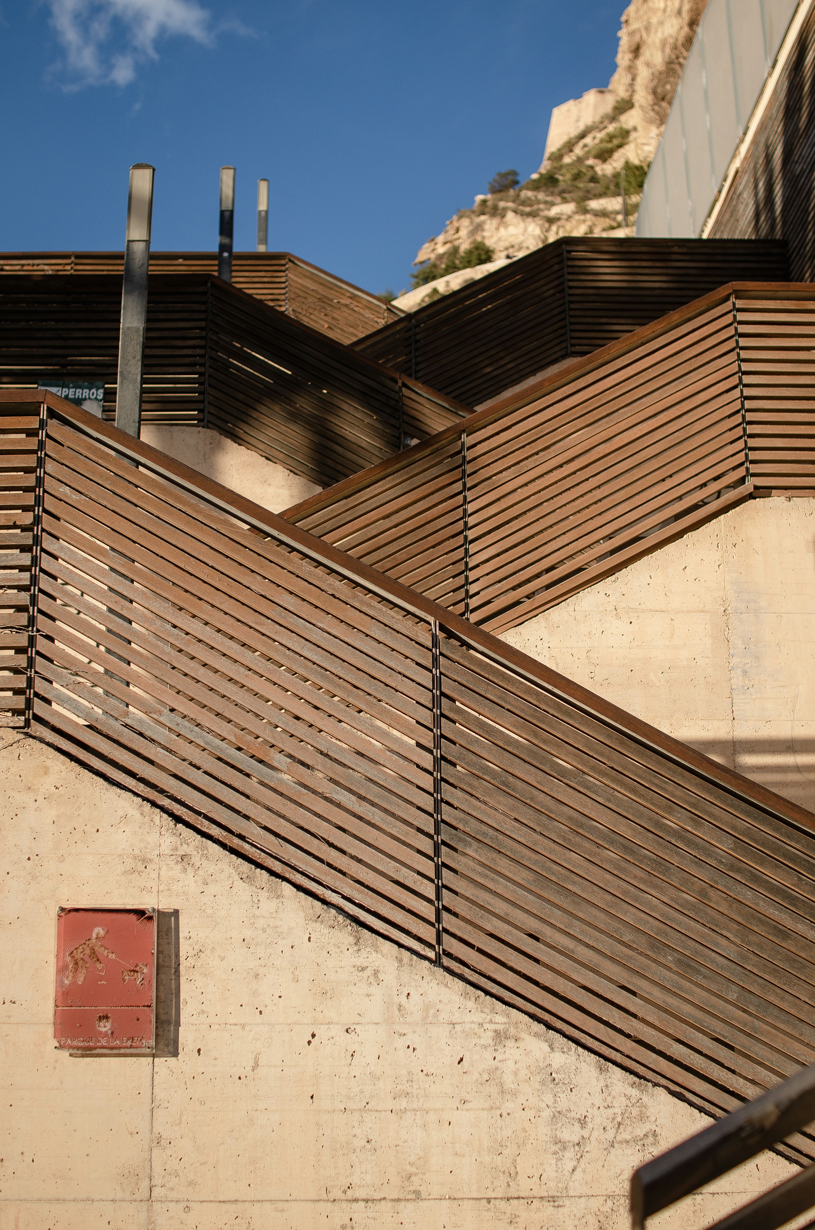 Terraced stairs of warm metal rails laddering up a sunlit concrete ramp
