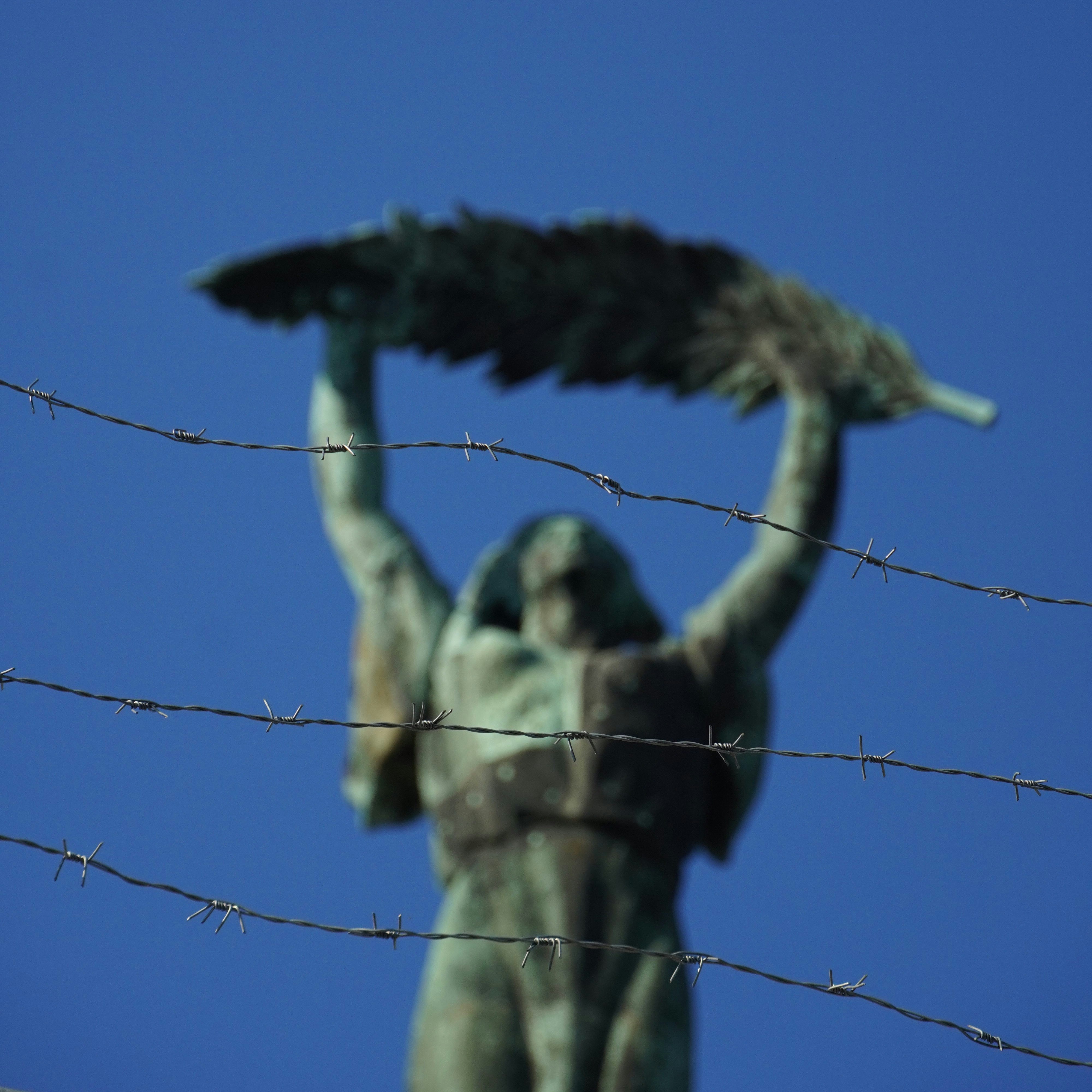 A statue of a man holding a bird behind a barbed wire fence photo ...