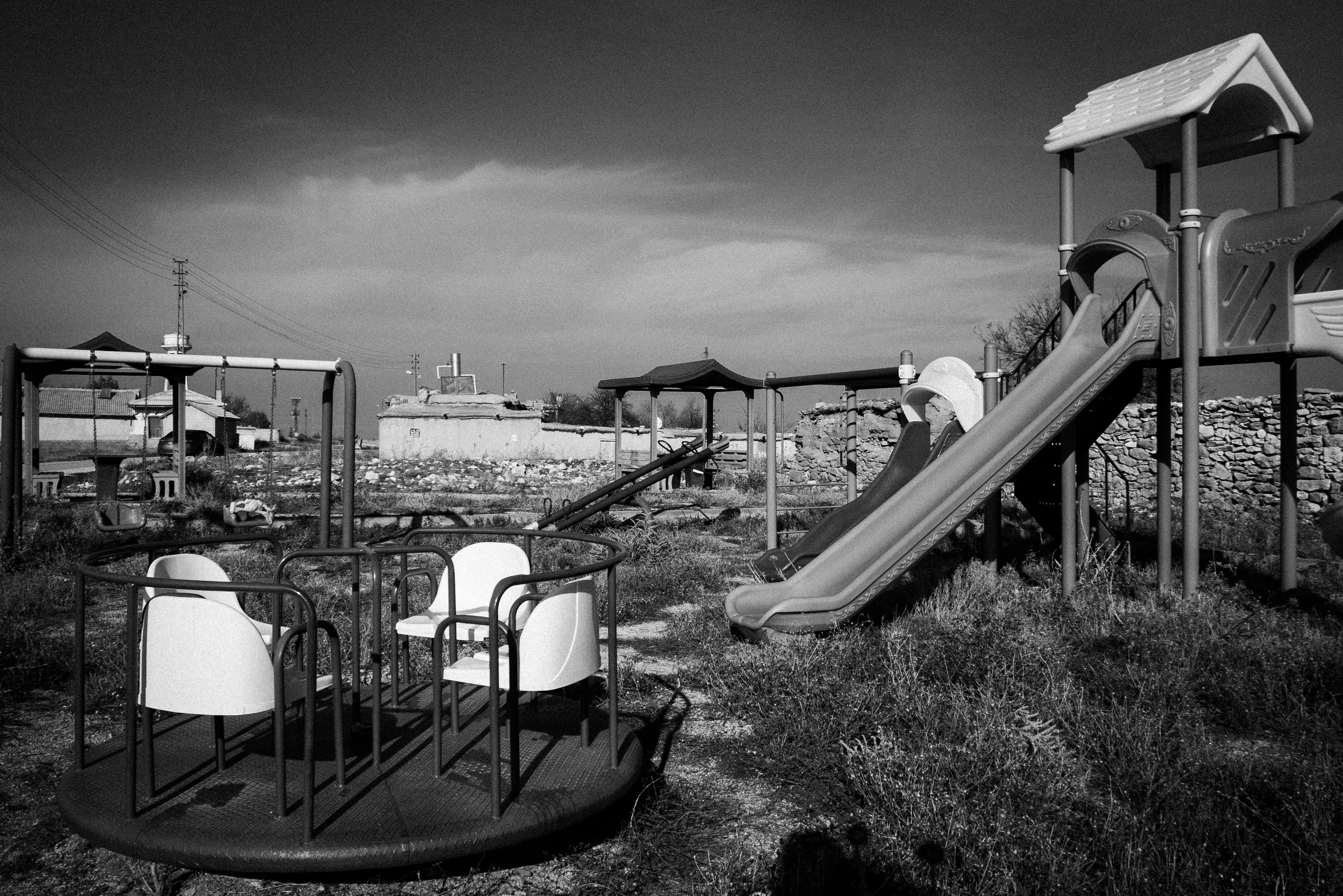 Abandoned playground with a slide and merry-go-round under a cloudy sky.