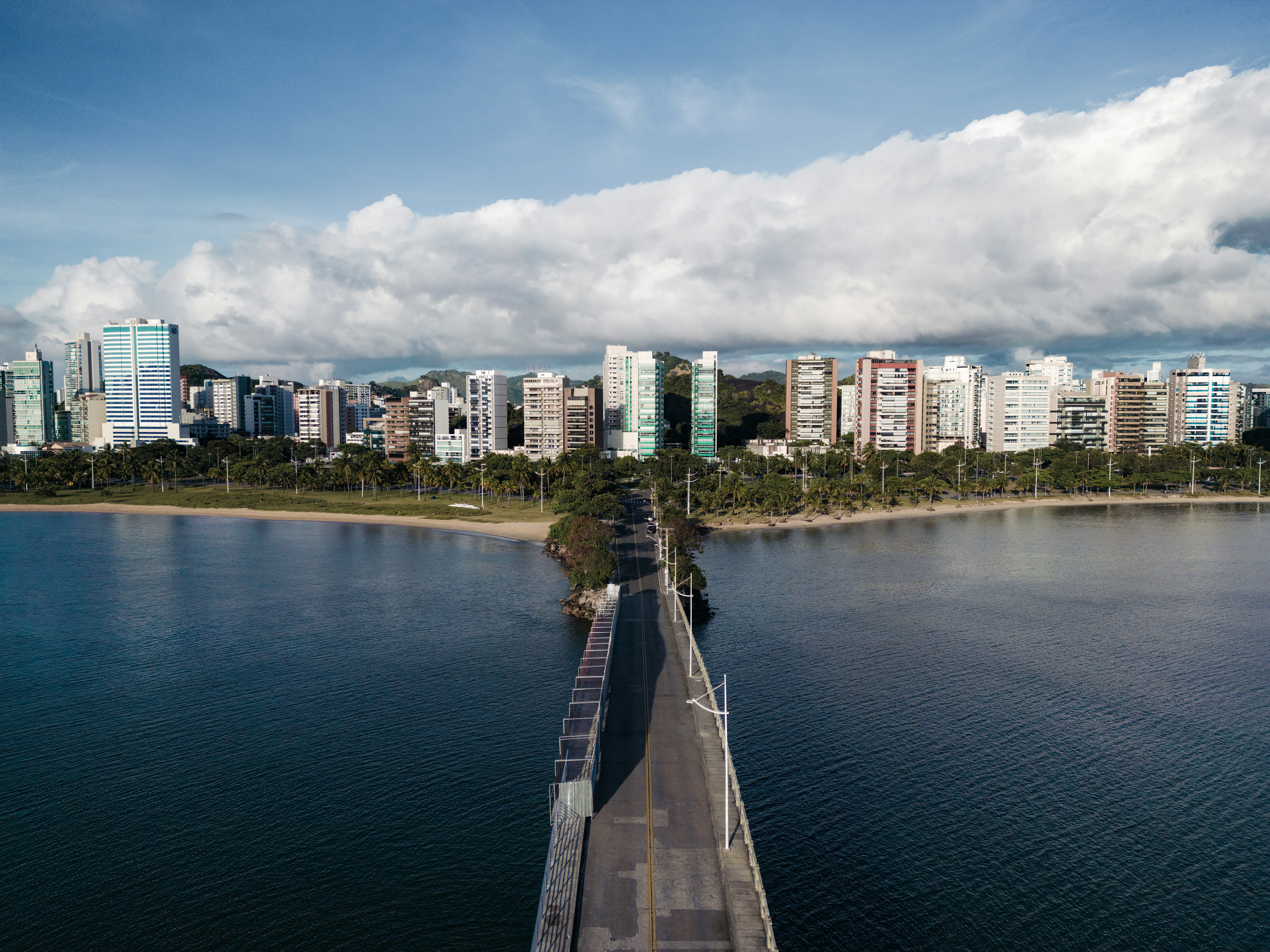 Aerial view of a bridge leading to a cityscape with tall buildings under a partly cloudy sky.