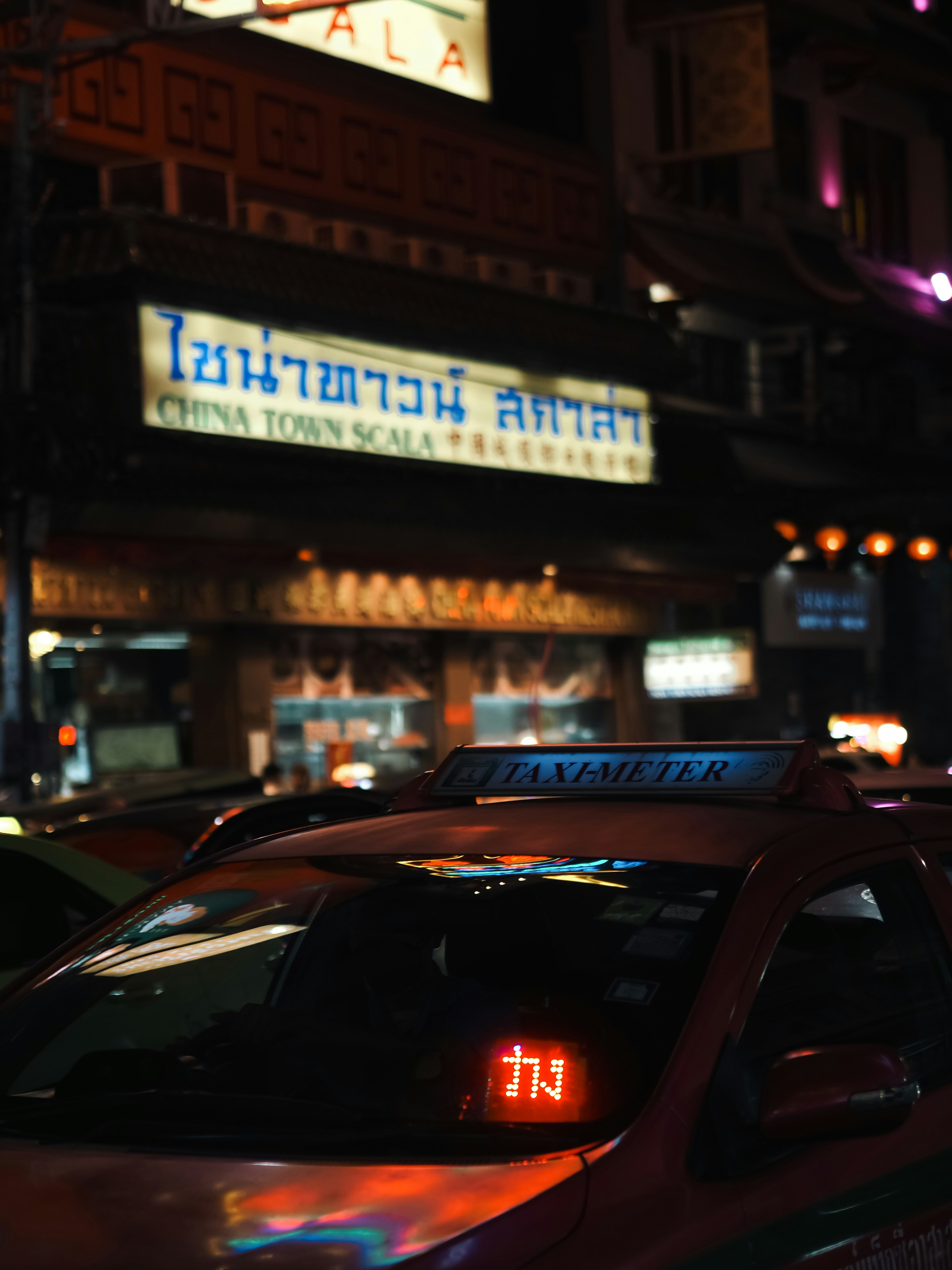 Illuminated taxi with a glowing taximeter against a backdrop of vibrant Chinatown signage at night.