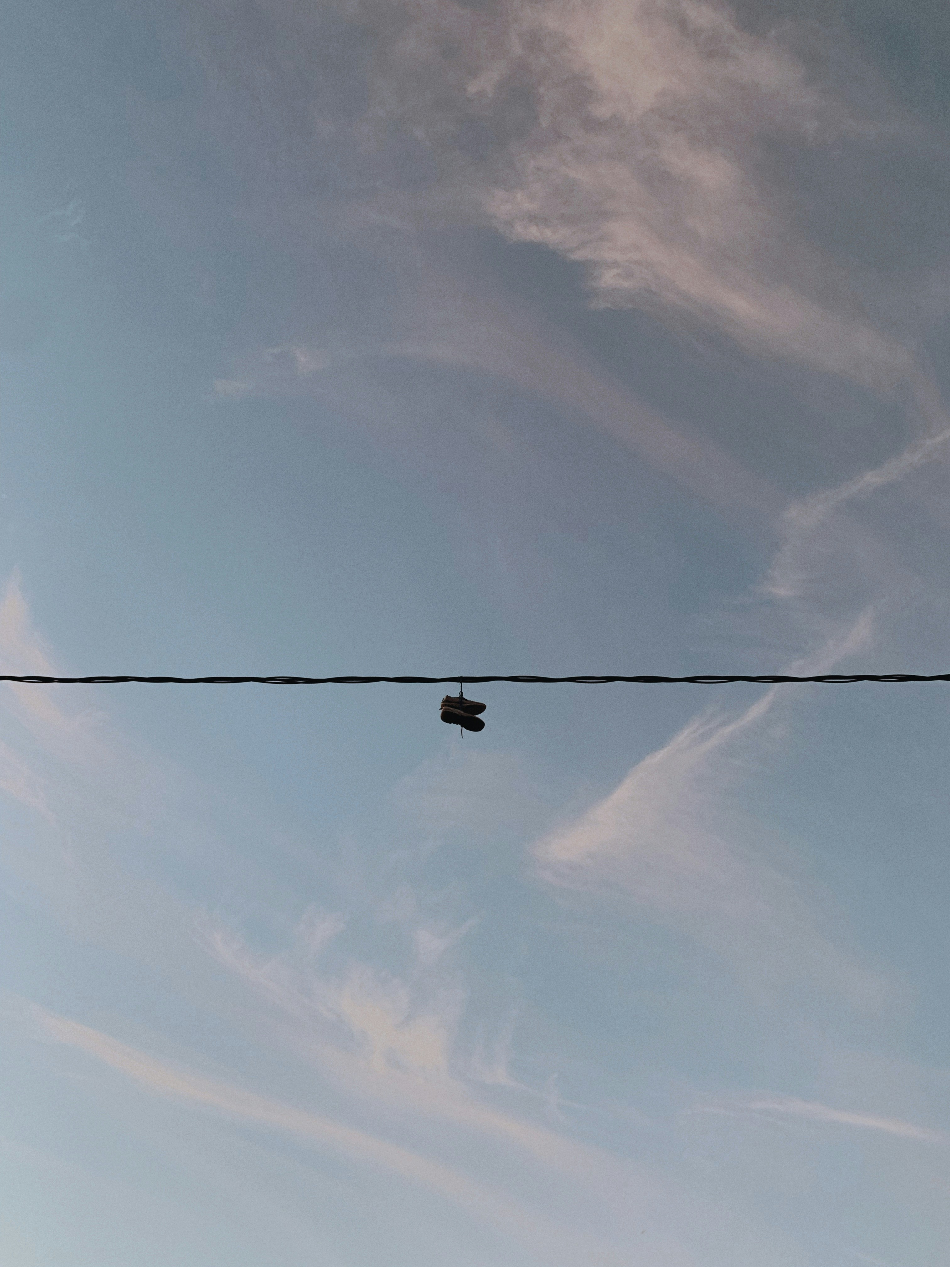 A lone pair of shoes suspended on a wire against a pale blue sky