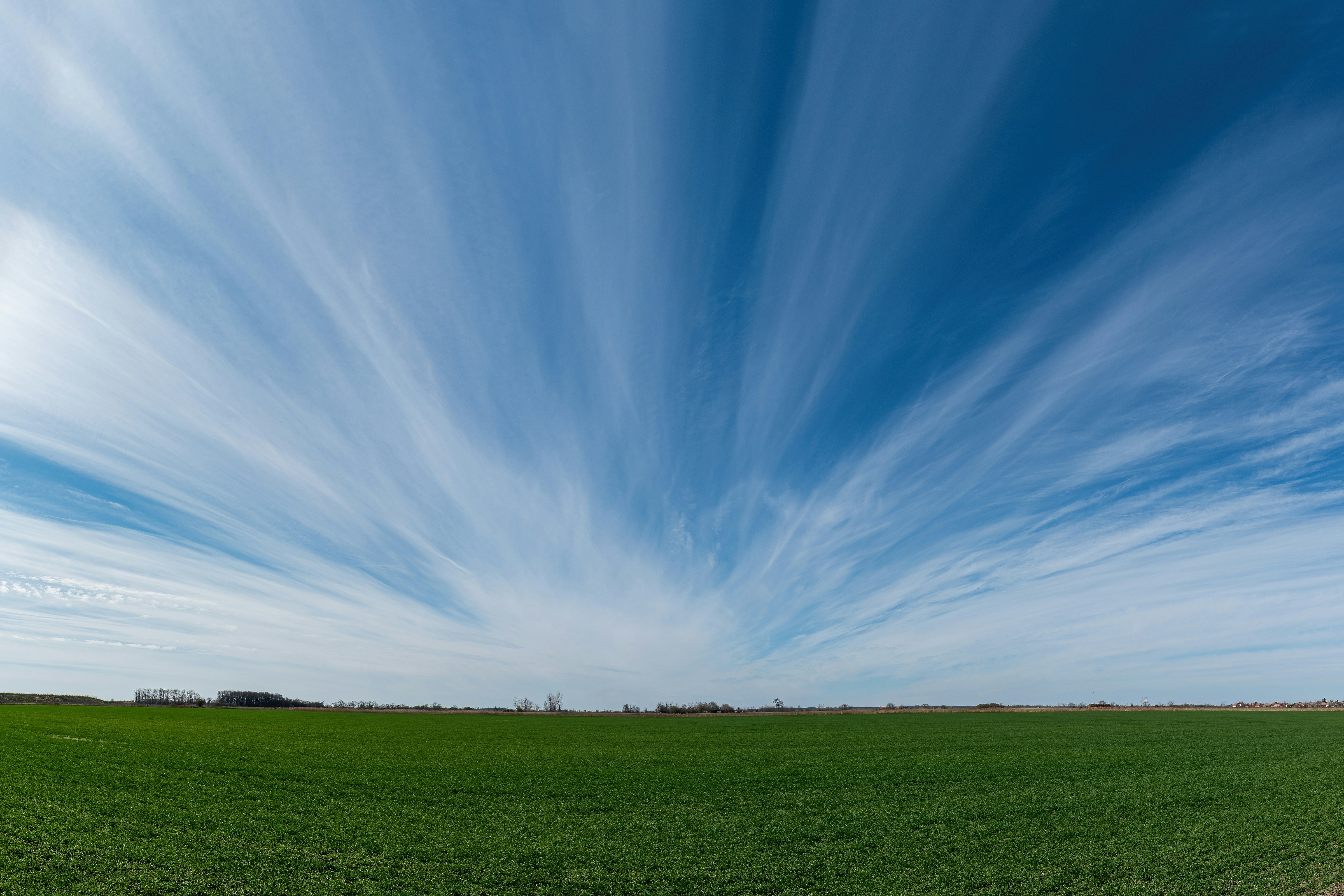 Vast green fields stretch under a dynamic sky filled with wispy clouds, showcasing the beauty of nature's palette.