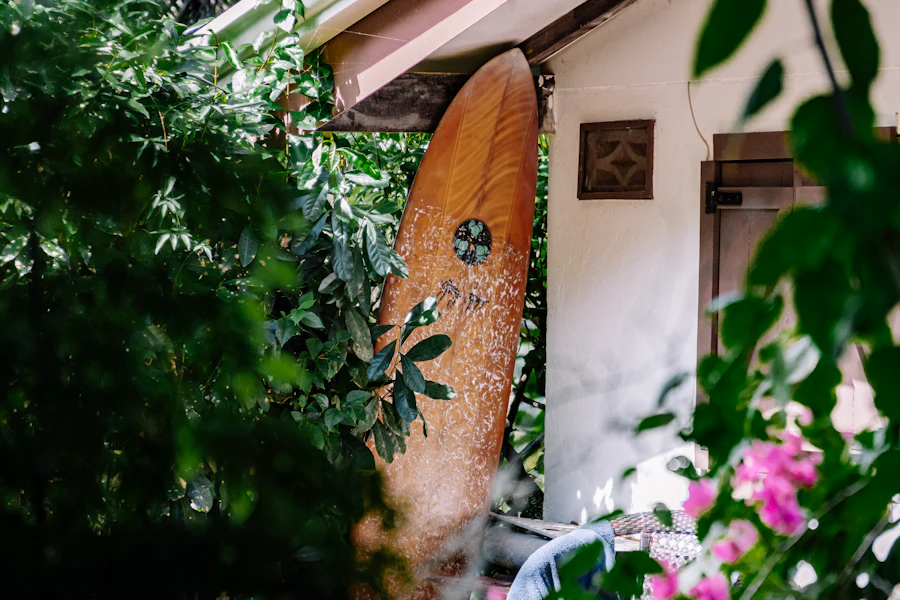 The surfboard waiting by the door ignites a feeling of excitement and anticipation as I start my day, ready to ride the waves. The connection with the ocean is priceless. | a surfboard leaning against the side of a house