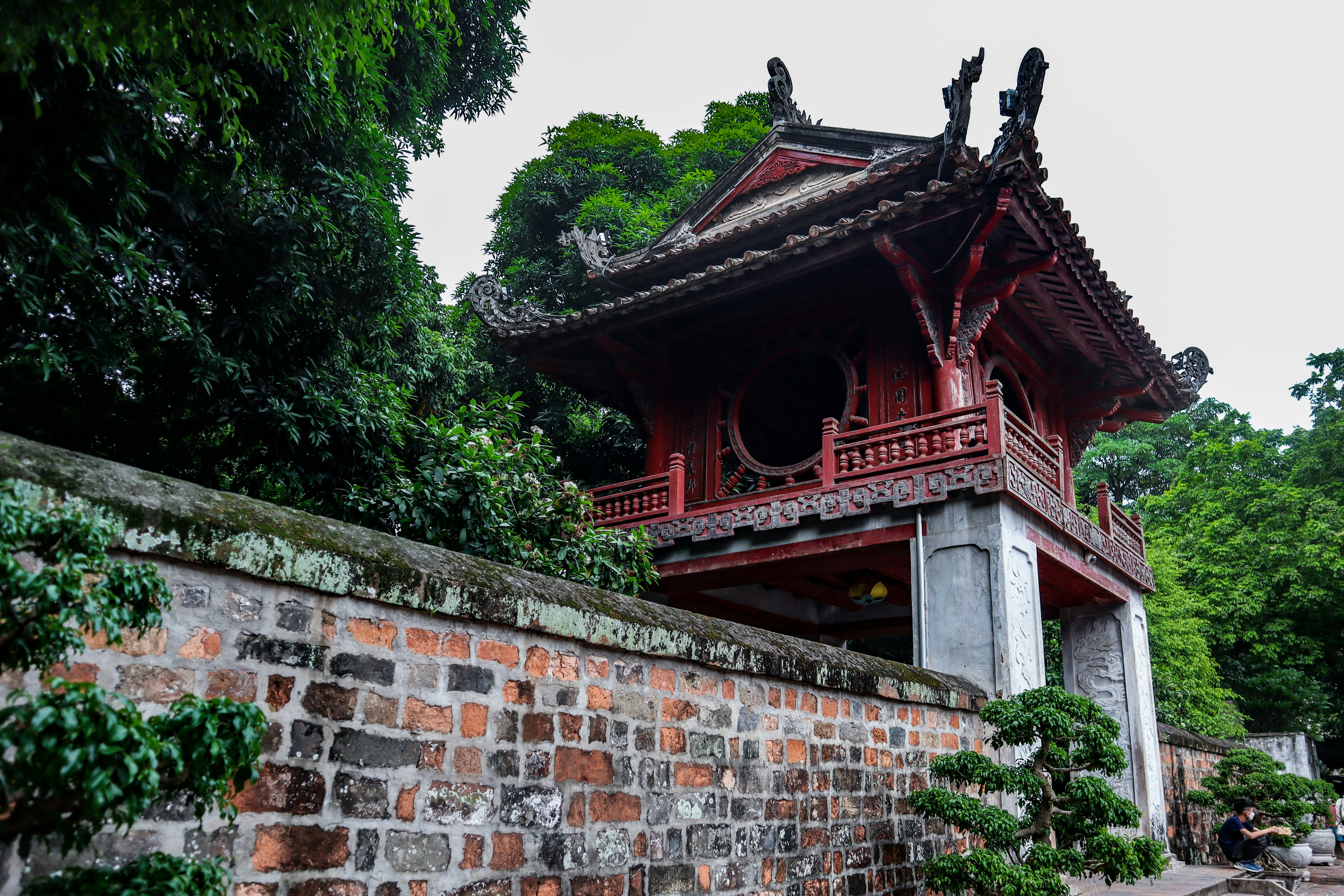 Intricately designed pavilion nestled among lush greenery and ancient stone walls, showcasing traditional architecture. A serene atmosphere envelops the scene.