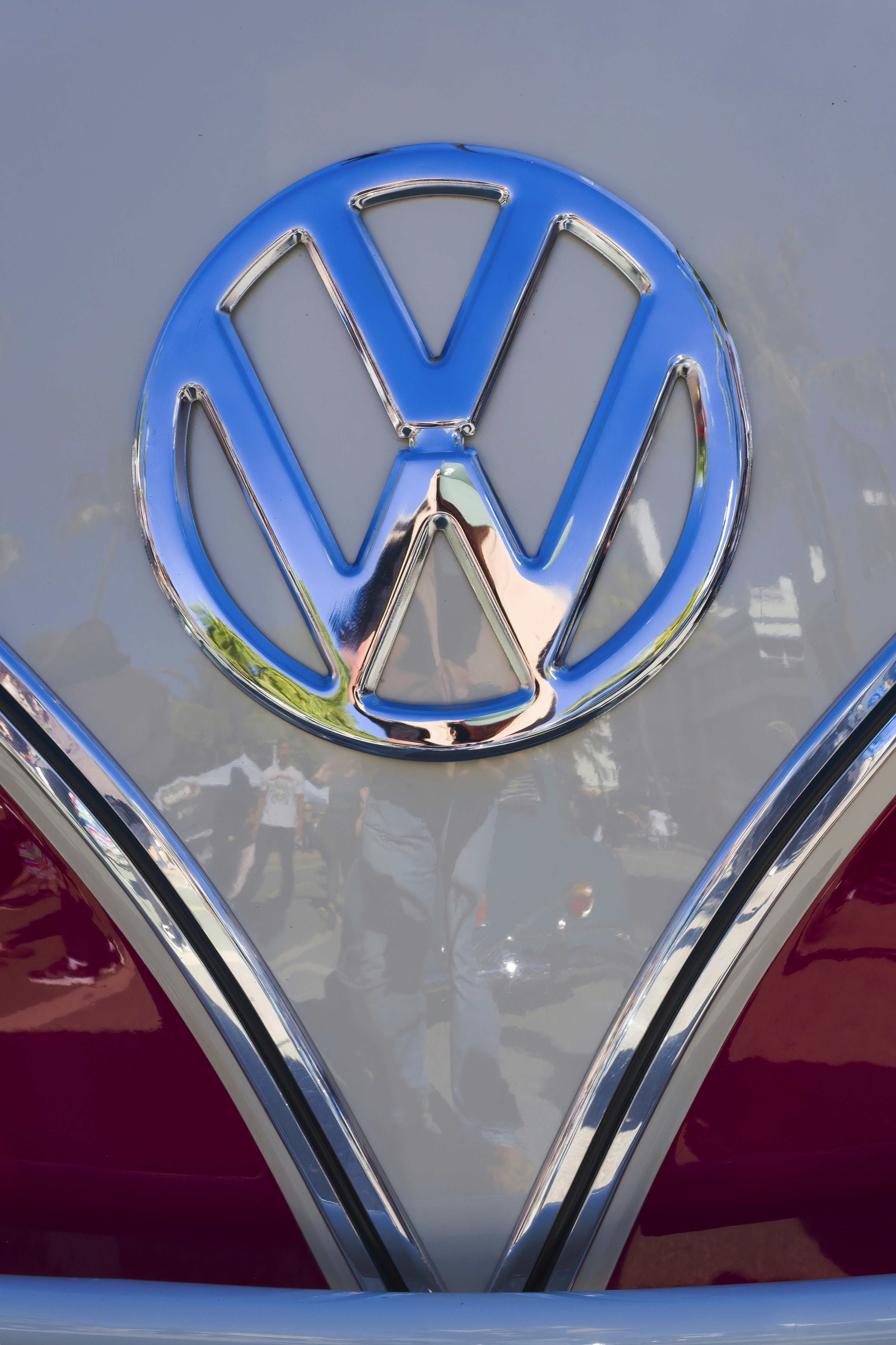 Chrome Volkswagen Emblem on a Vintage Van - A close-up photograph of a chrome Volkswagen emblem on the front of a vintage van. The emblem is shiny and reflects the surrounding environment. The van's body is painted in a combination of white and red.