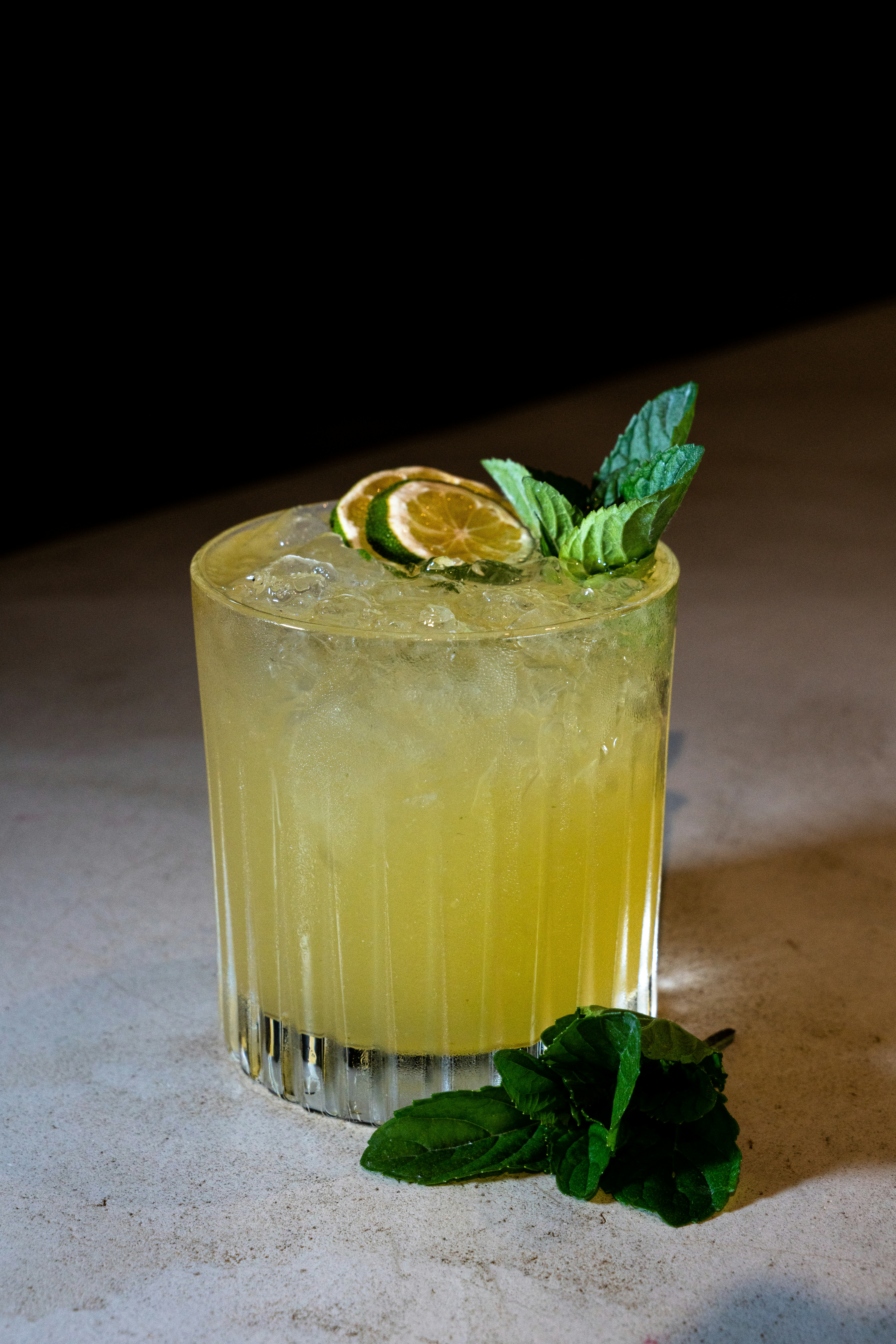A refreshing cocktail garnished with lime slices and mint leaves, served in a textured glass on a neutral surface.
