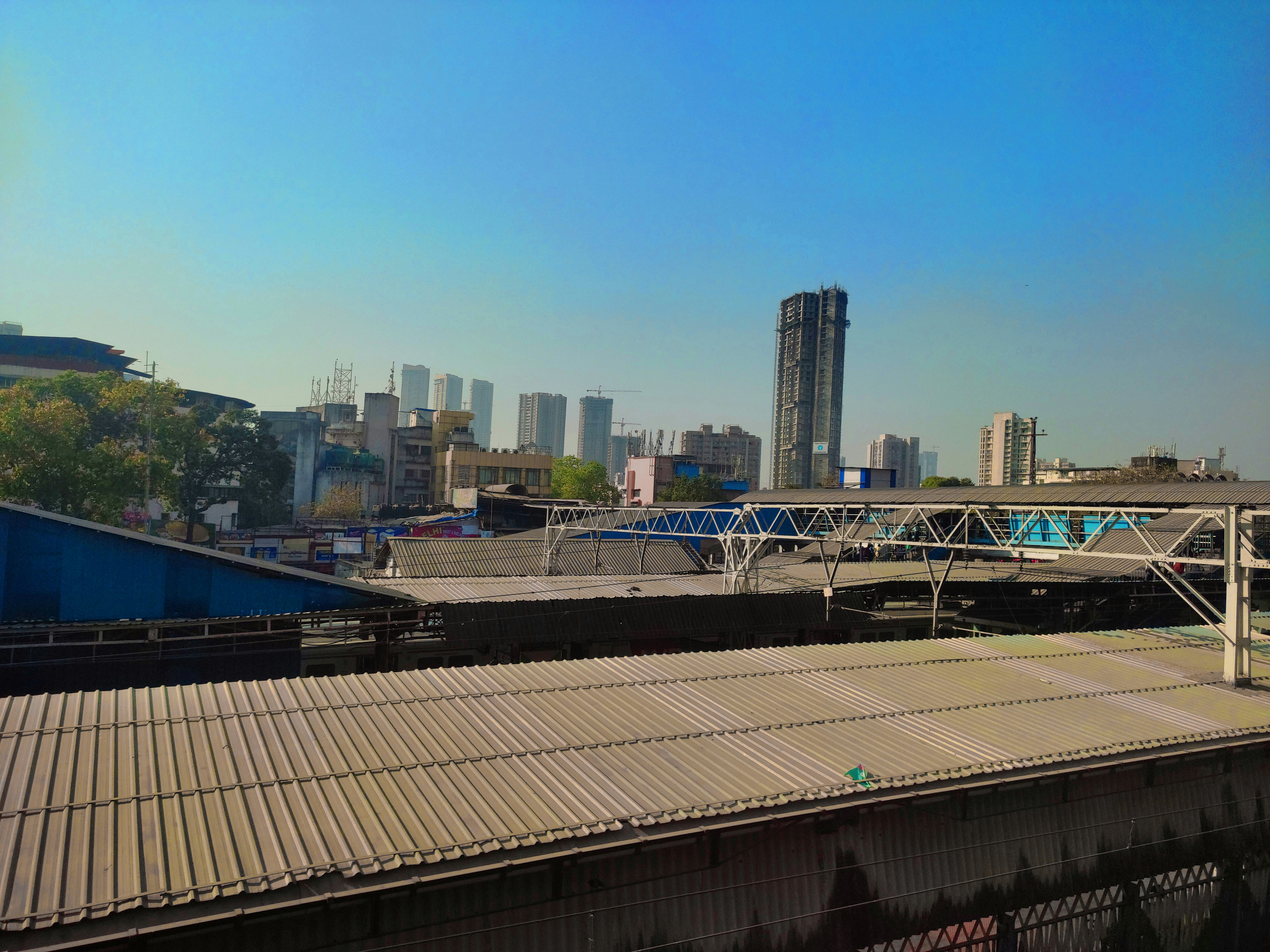 A panoramic view of urban rooftops and distant skyscrapers under a clear blue sky, illustrating the layered complexity of city architecture.