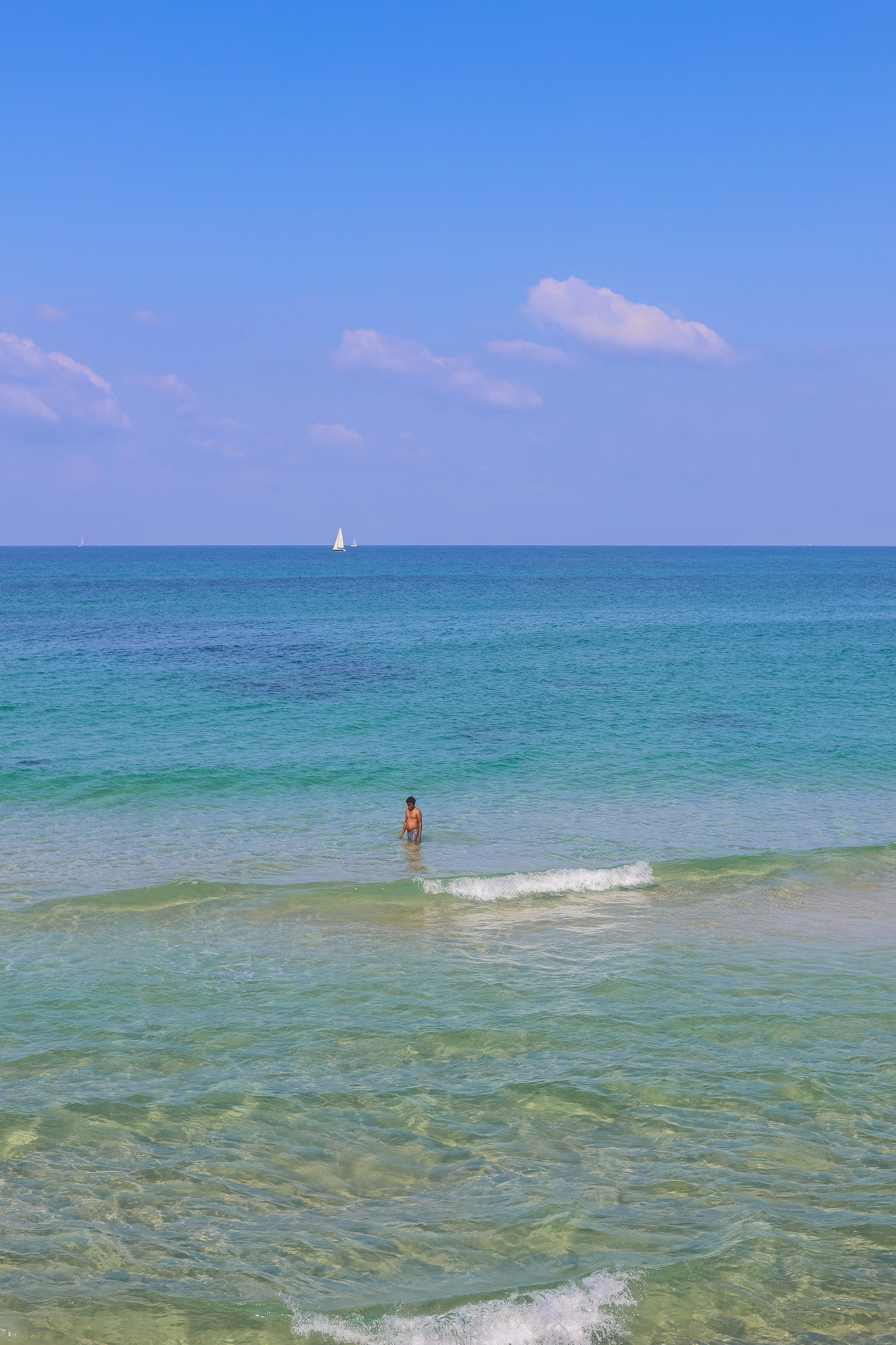 Solitary Swimmer at the Edge of a Turquoise Sea, with a Distant Sail on the Horizon