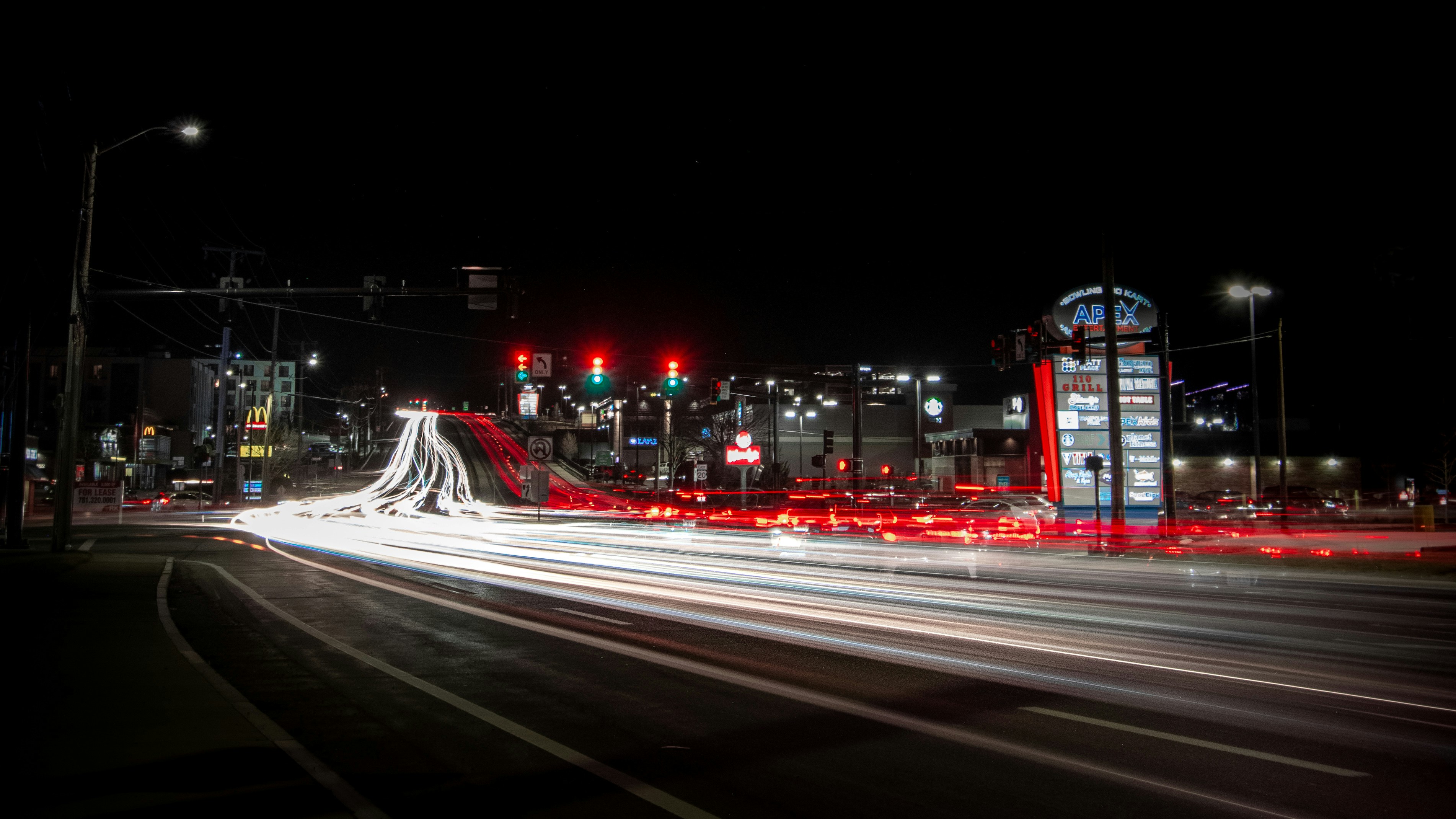 Dynamic light trails from vehicles weave through a bustling urban intersection at night, highlighting the vibrant city life.