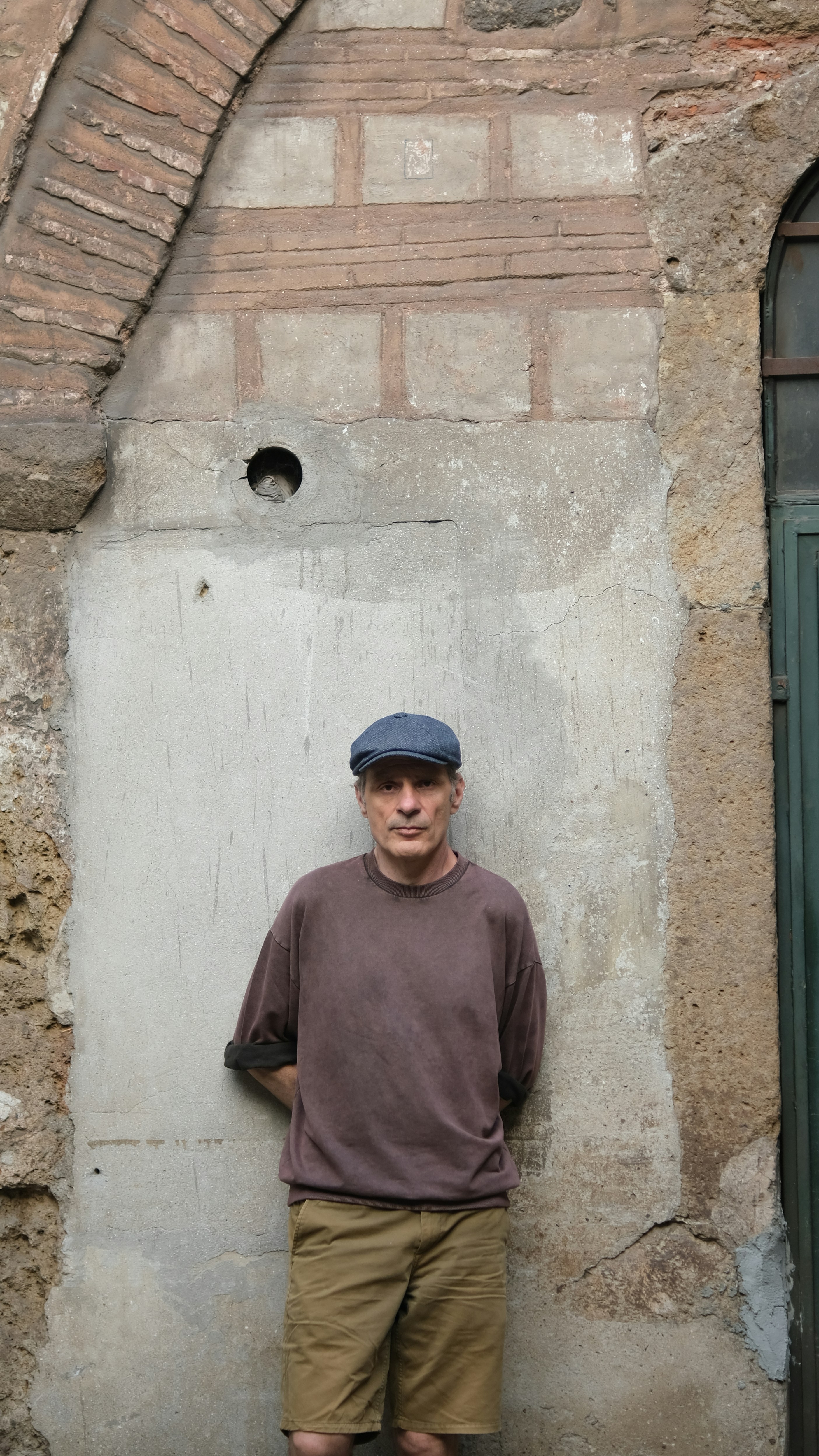 Urban Portrait in Weathered Stone: A Man in a Maroon Sweatshirt at the Arch-Wall