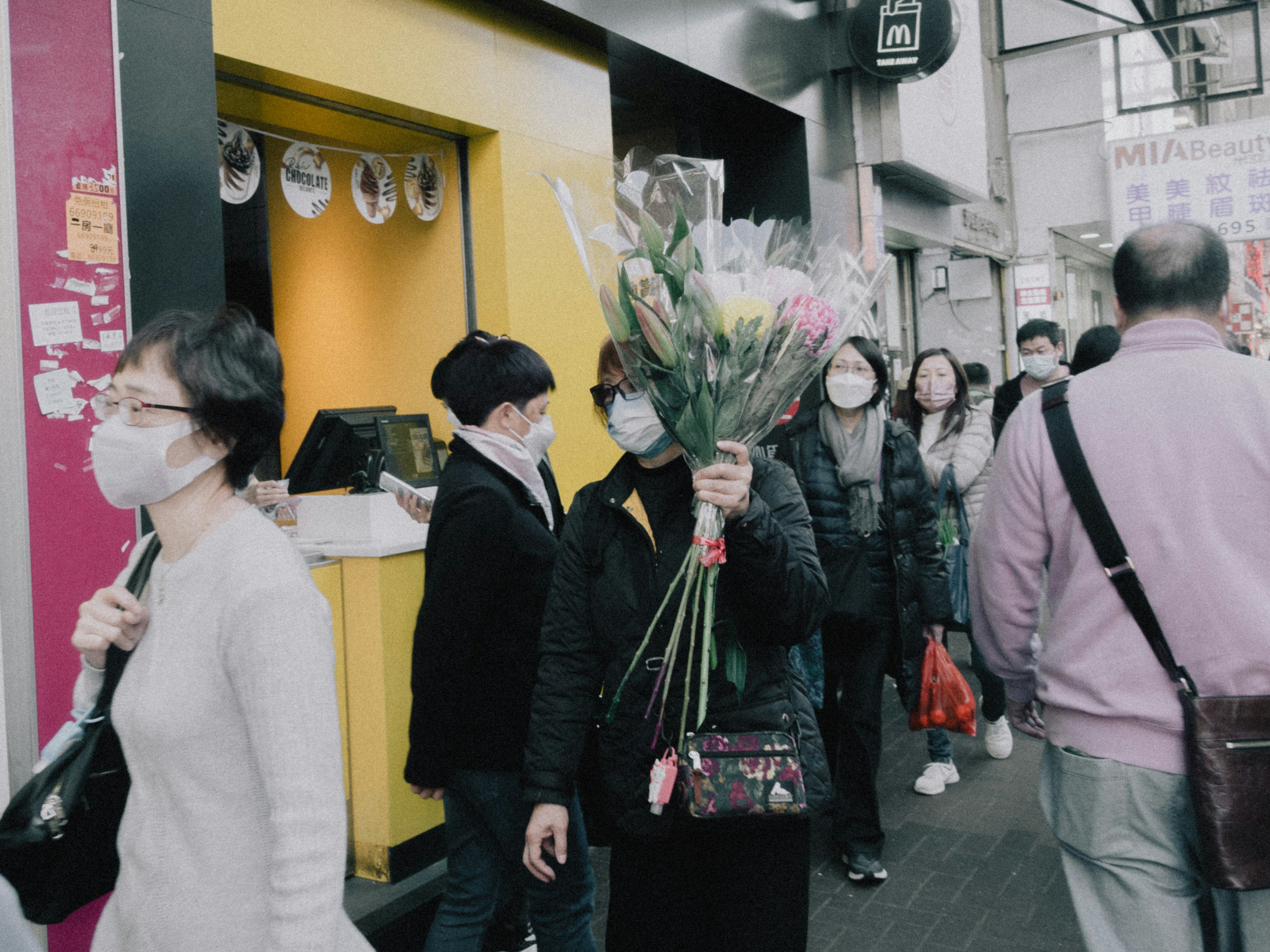 Bouquet Between Masks: A Candid Moment by the Yellow Shopfront