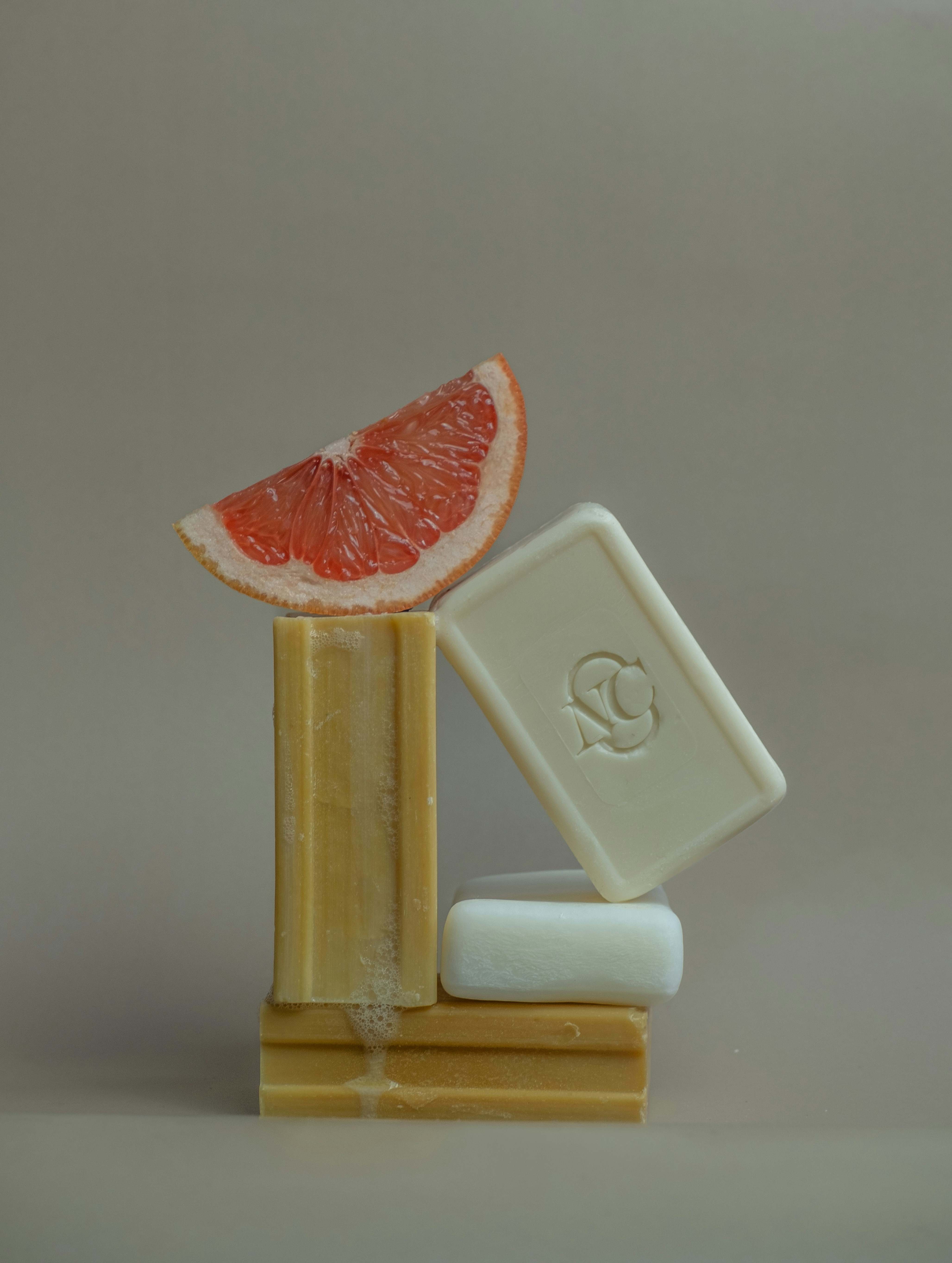 Artistic arrangement of soap bars and a grapefruit slice, showcasing a harmonious blend of colors and textures. The composition emphasizes minimalism and freshness.