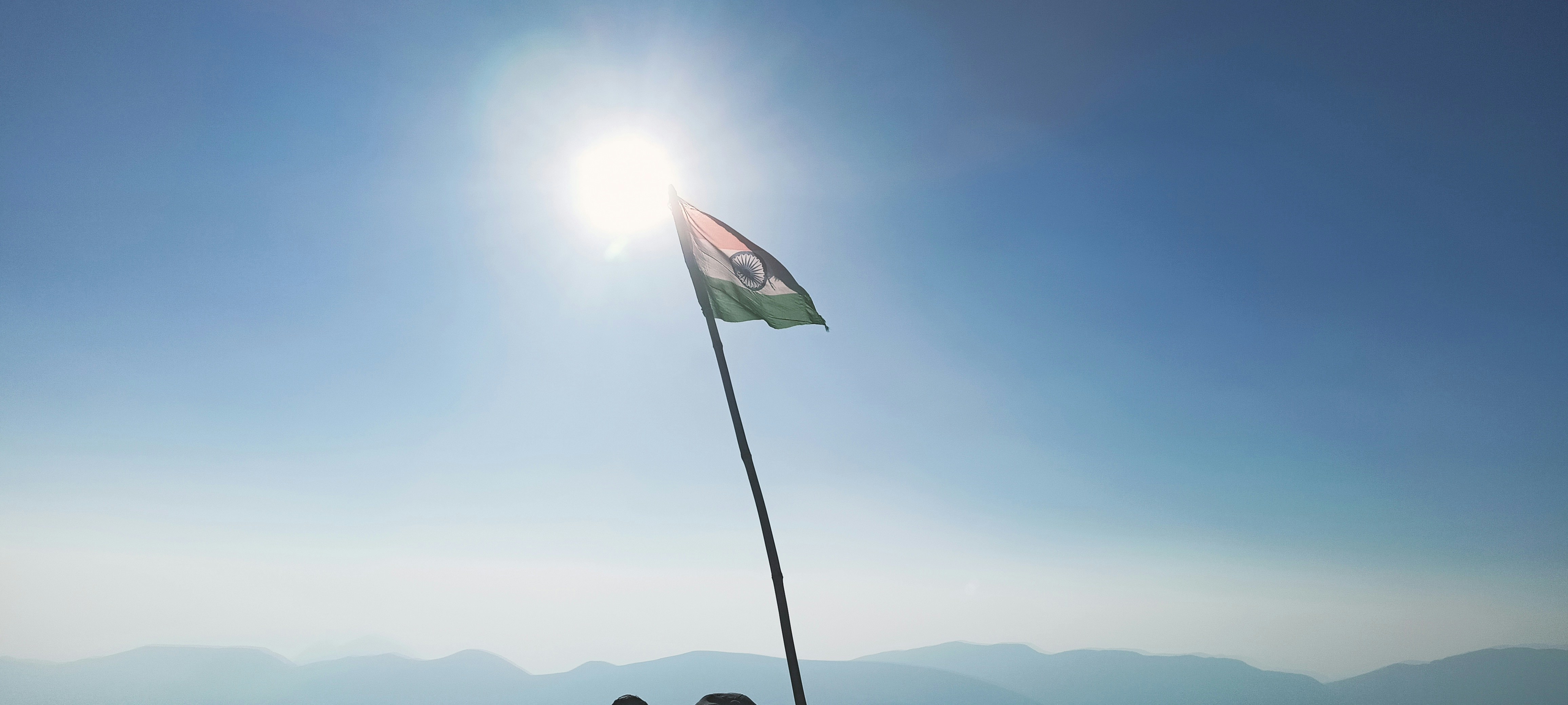 Flagpole Against a Radiant Alpine Sun Over a Quiet Mountain Horizon