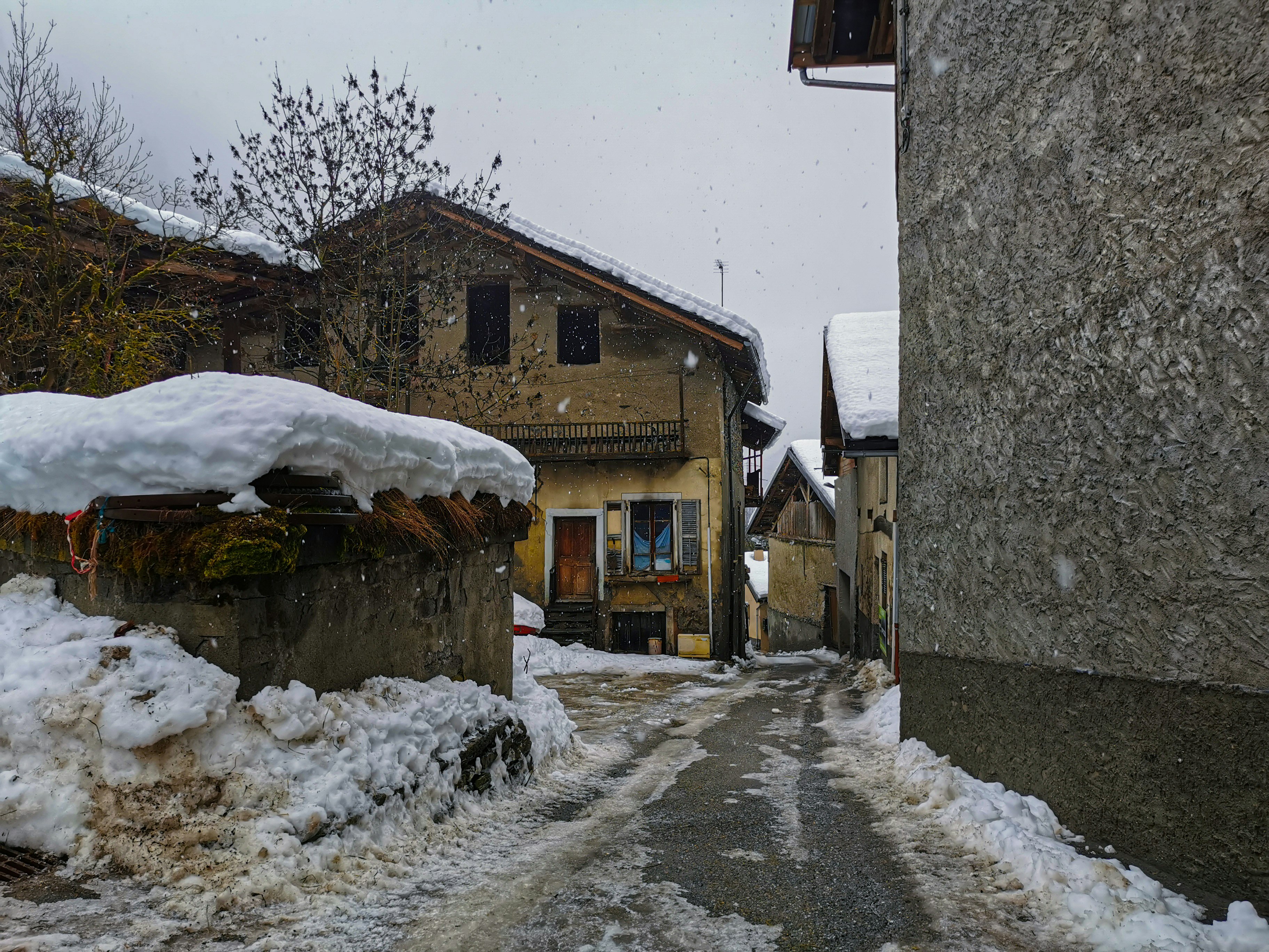 Snowbound village street photograph with snow piled along the sides and rustic houses receding into a narrow, snow-dusted lane.