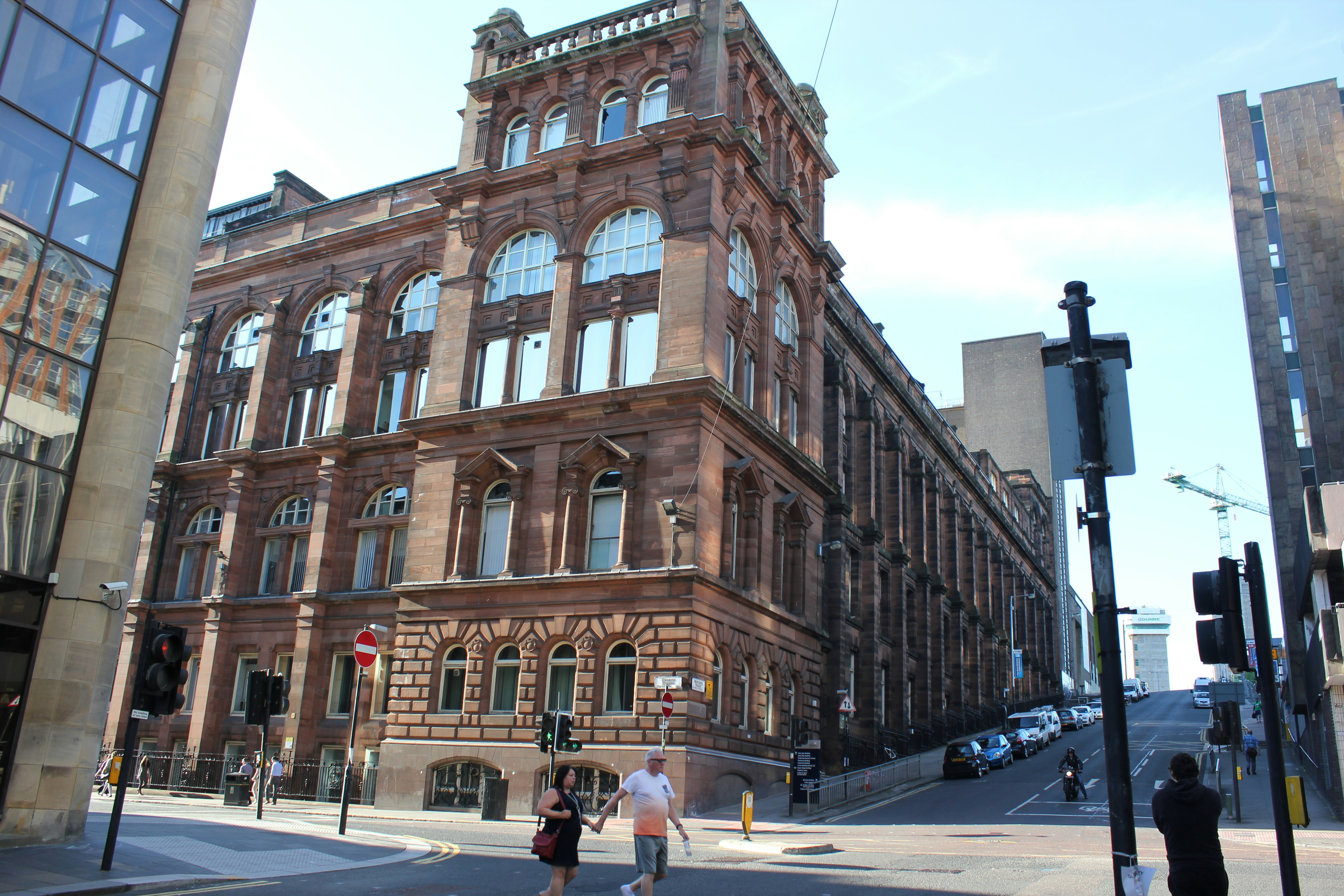Two people crossing the street in front of a large building photo ...