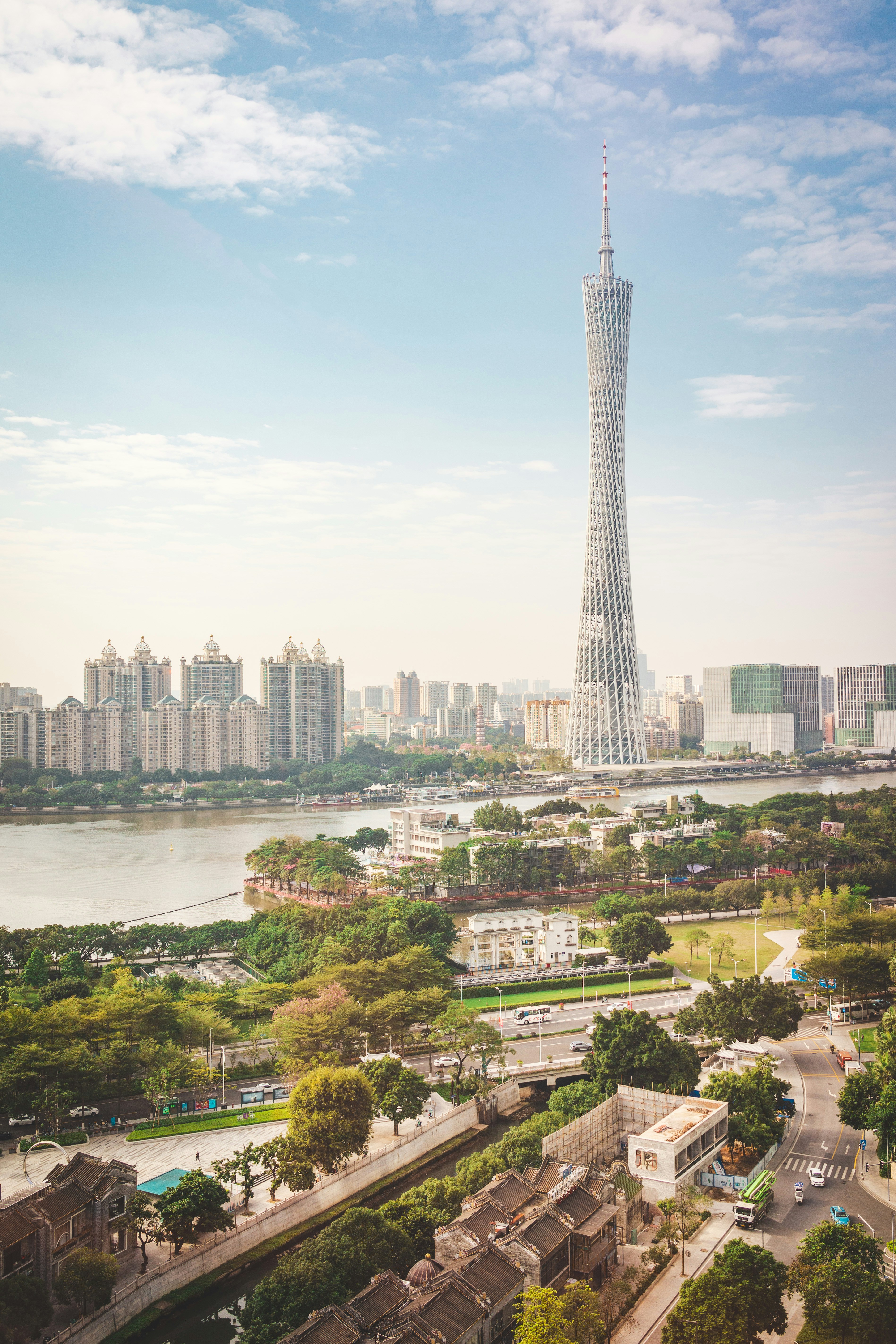 The iconic Guangzhou Tower rises above the cityscape, framed by a serene river and lush greenery. A blend of modern architecture and nature's tranquility.