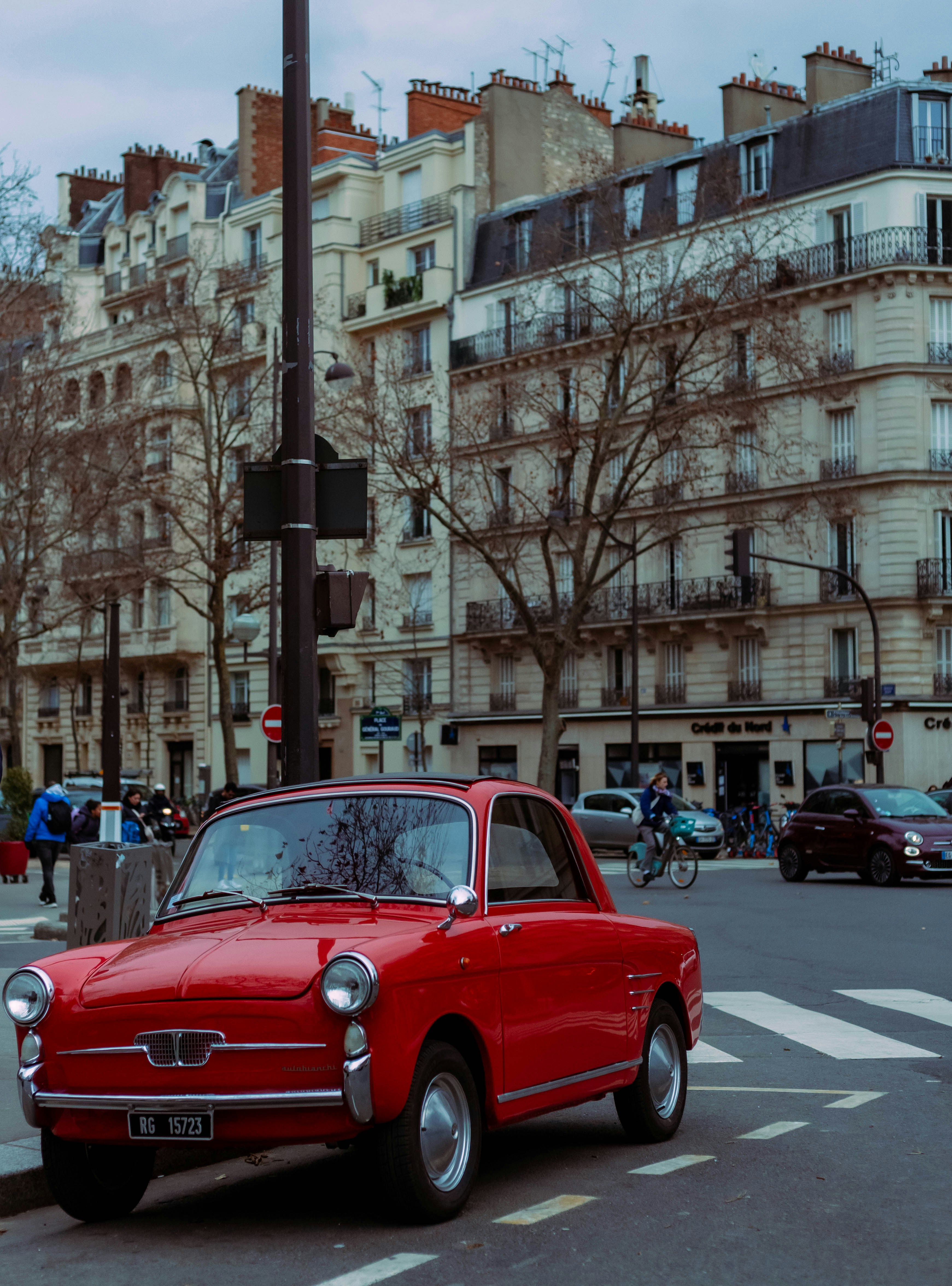 Classic red car parked on a bustling street in Paris, surrounded by elegant buildings and trees.