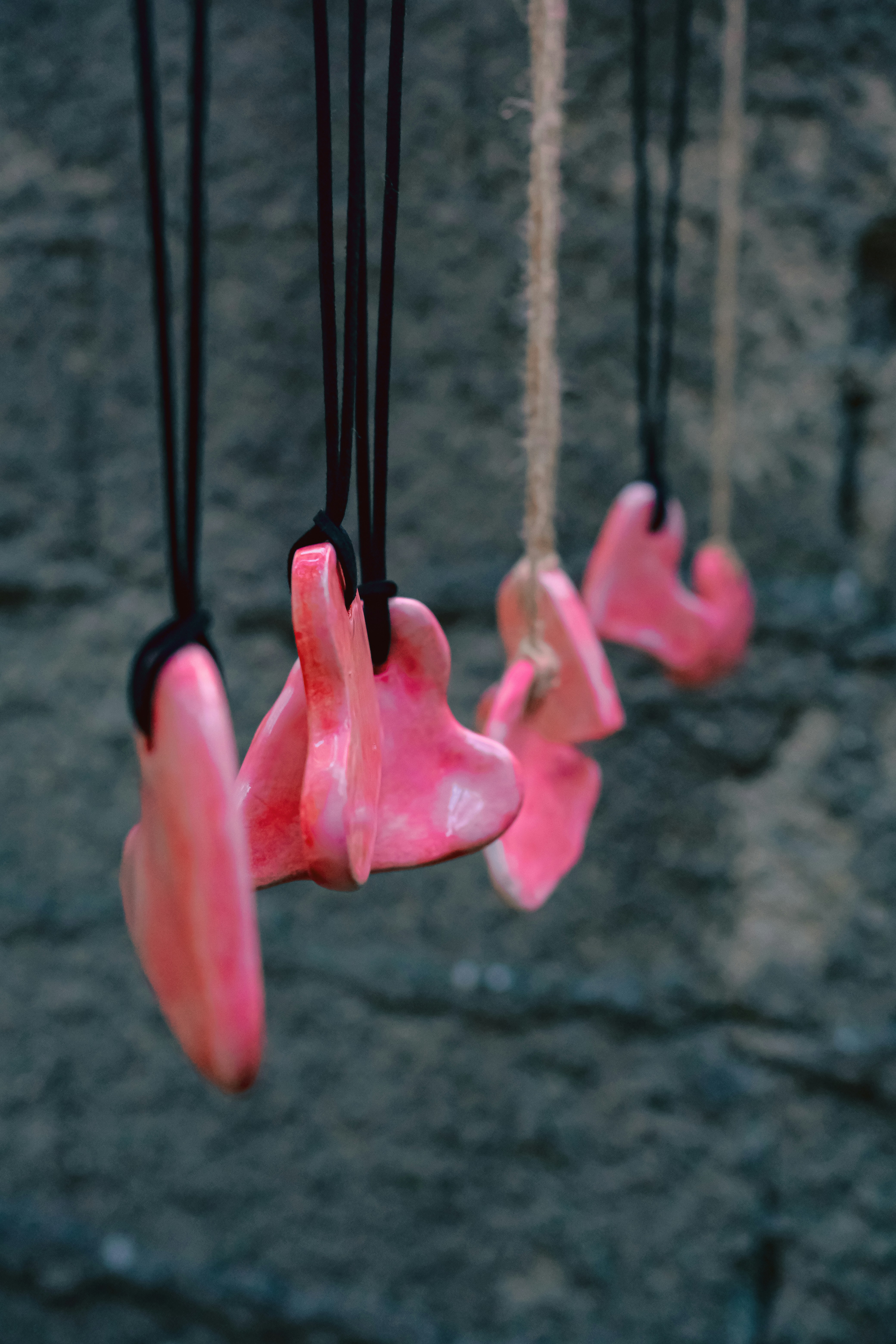 Pink Petal Pendants on Black Cords Before a Weathered Stone Wall