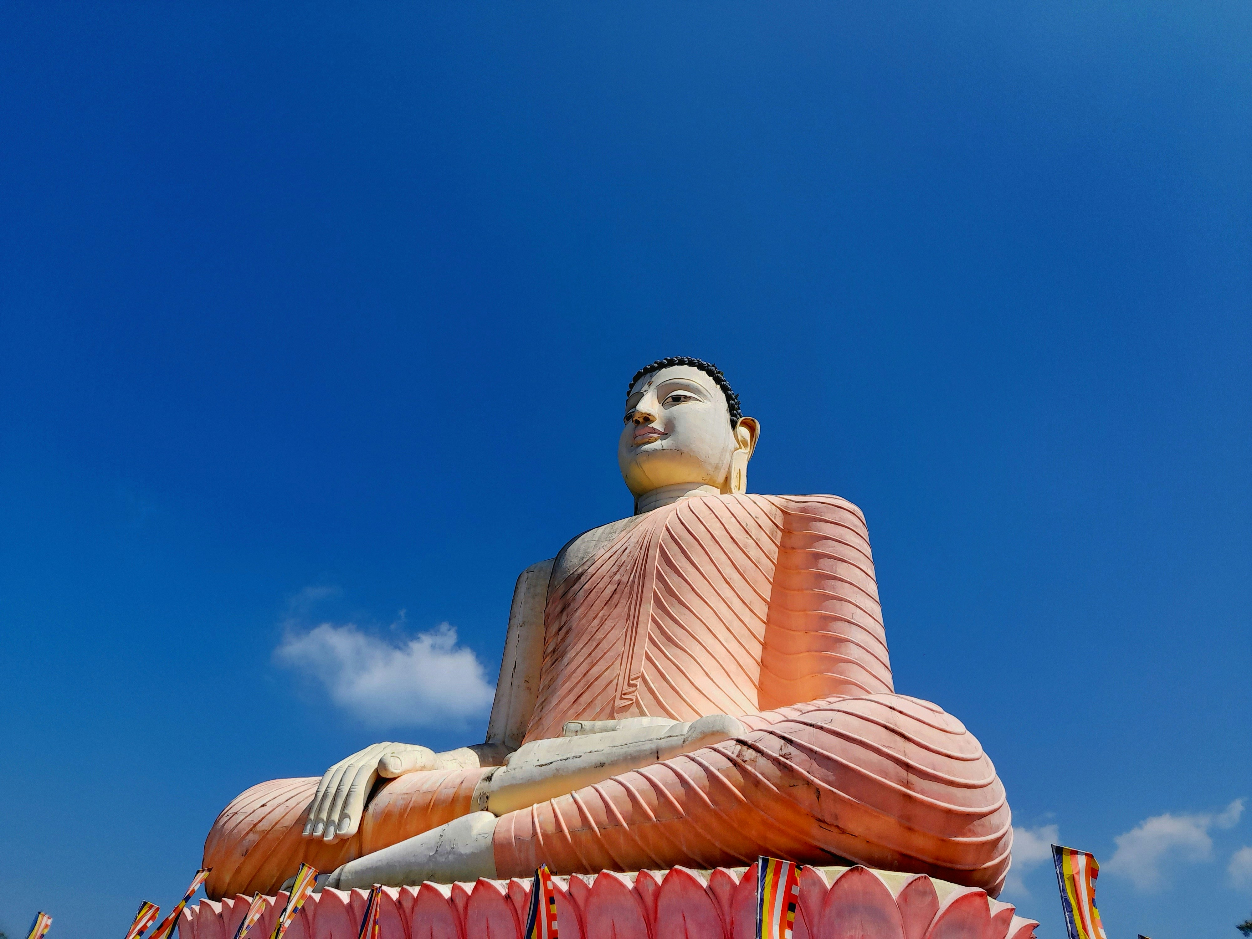 Majestic seated Buddha statue against a clear blue sky, adorned with colorful flags at its base.