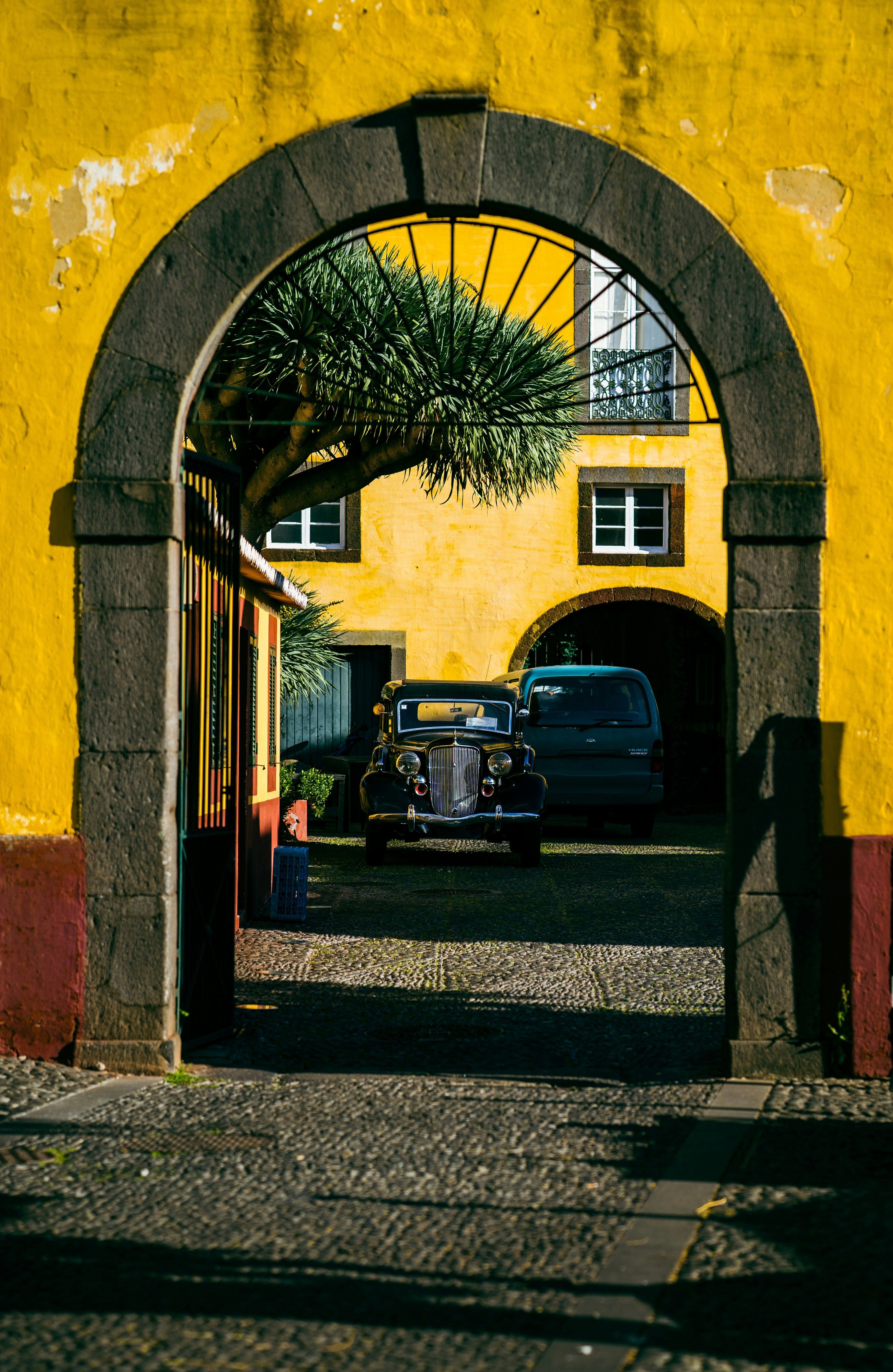 Archway of Sunlit Yellow: A Vintage Car Framed in a Quiet Courtyard