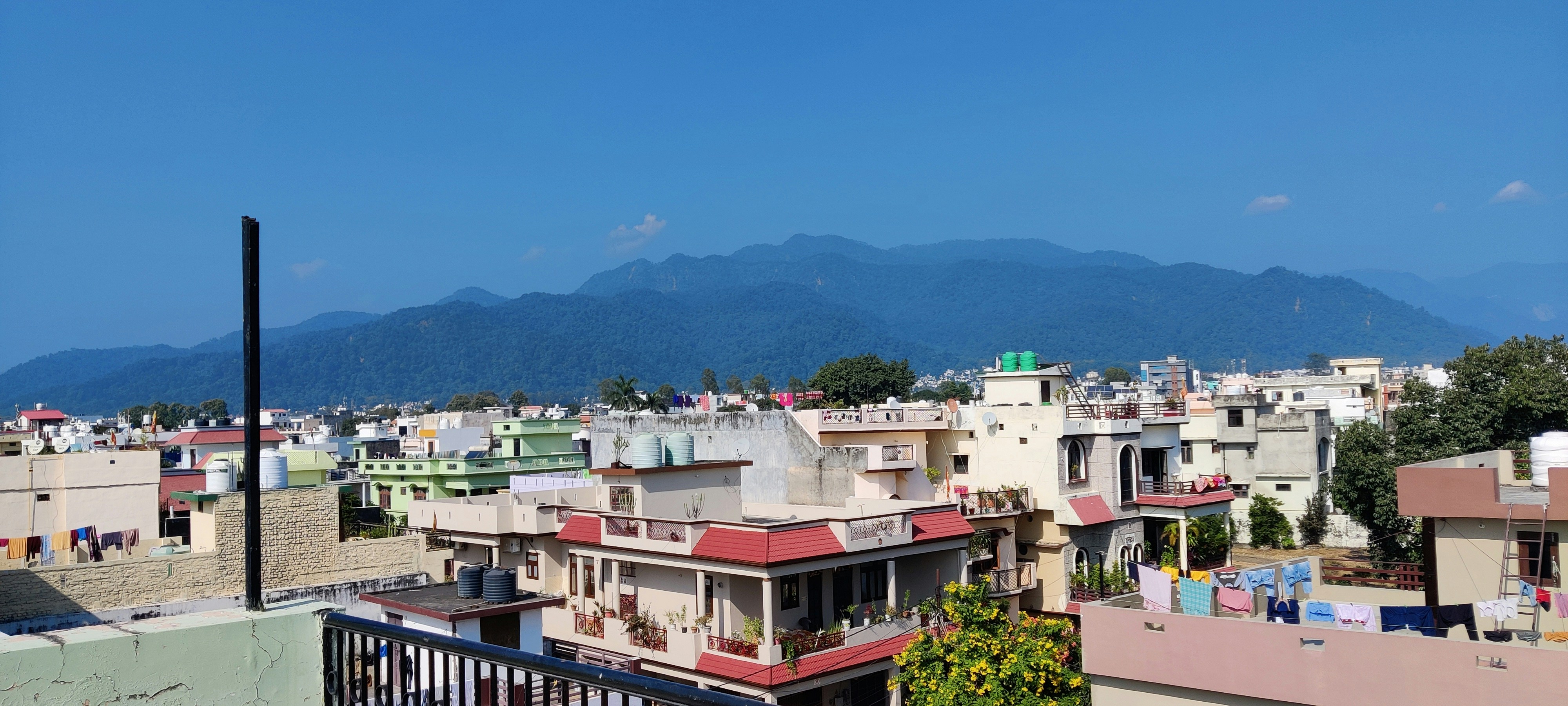 Cityscape with colorful rooftops framed by distant blue mountains under a clear sky.