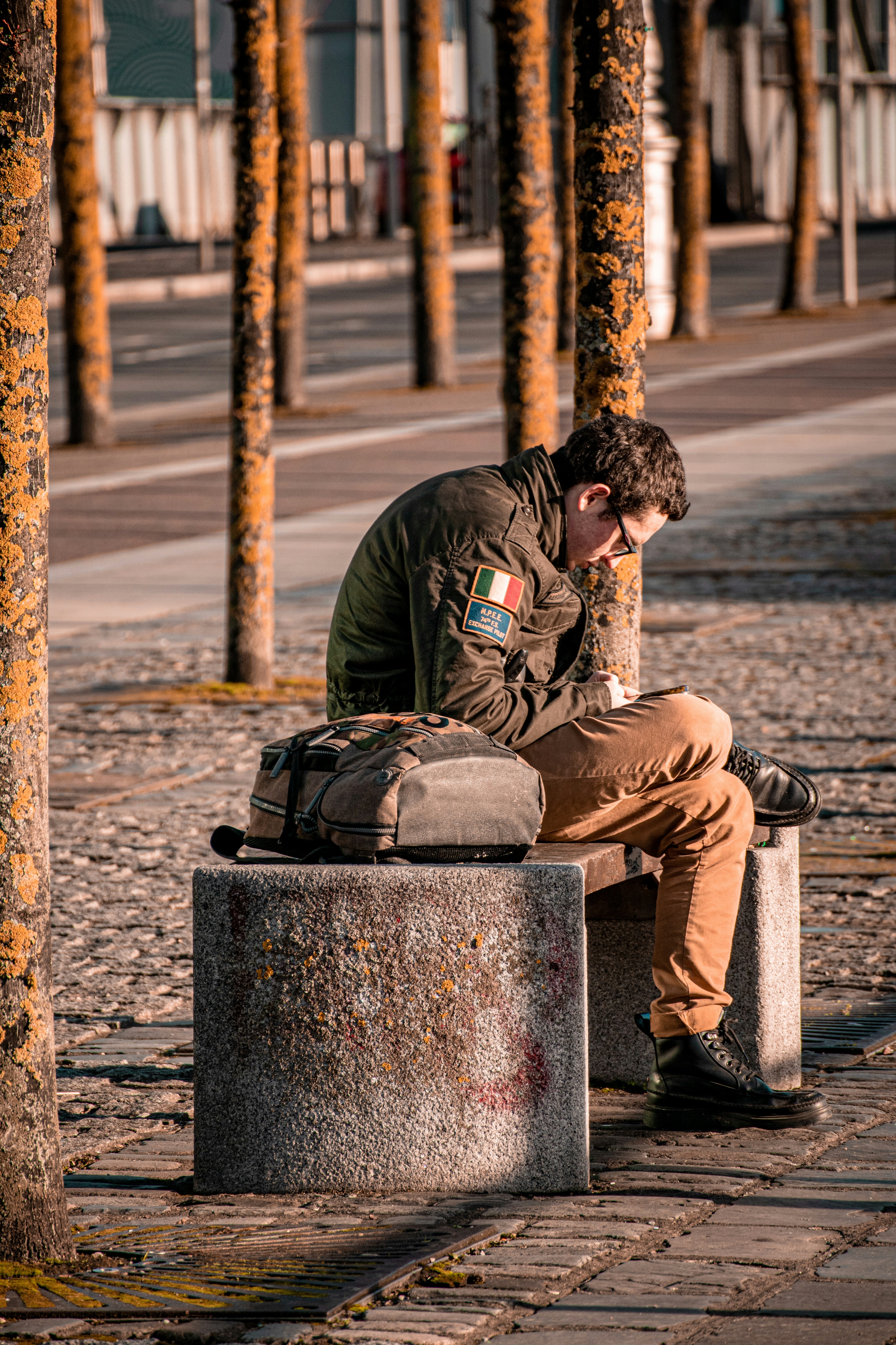 Man in a green jacket lost in thought on a sunlit urban bench