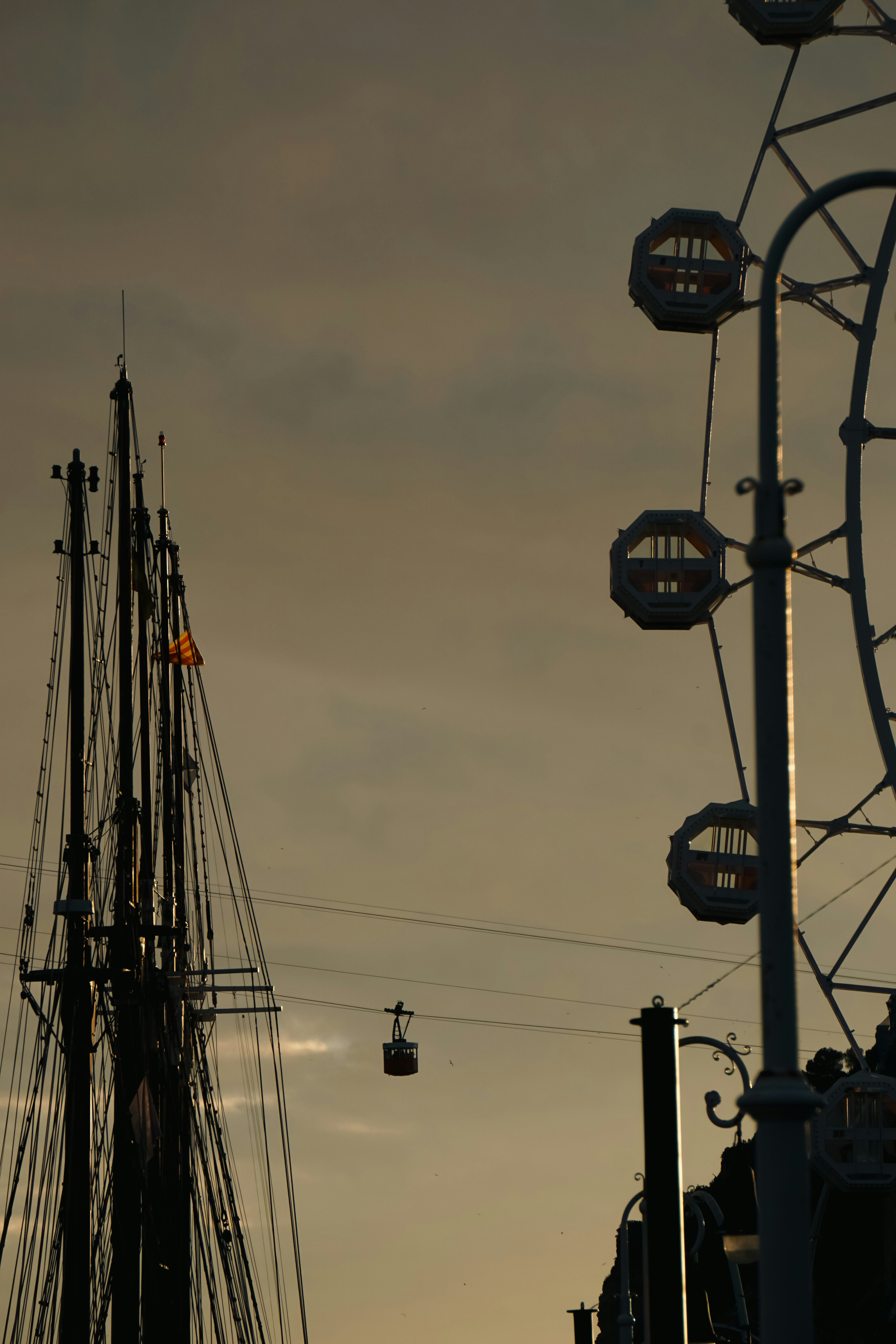 Midline Glide at Dusk: Gondola Between Rigging and a Ferris Wheel Silhouette