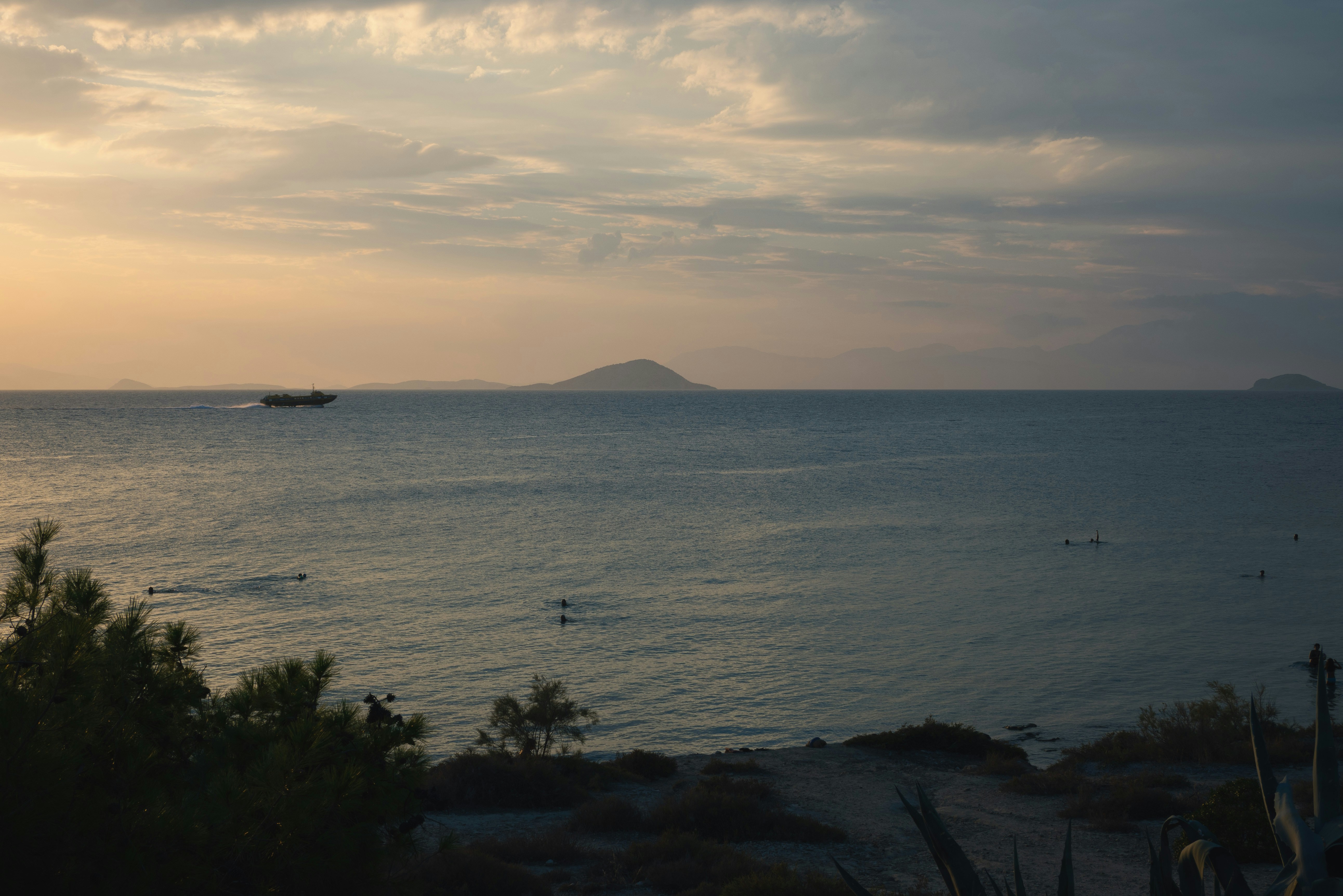 A tranquil seascape at dusk, featuring a boat gliding across calm waters with distant islands silhouetted against the horizon.