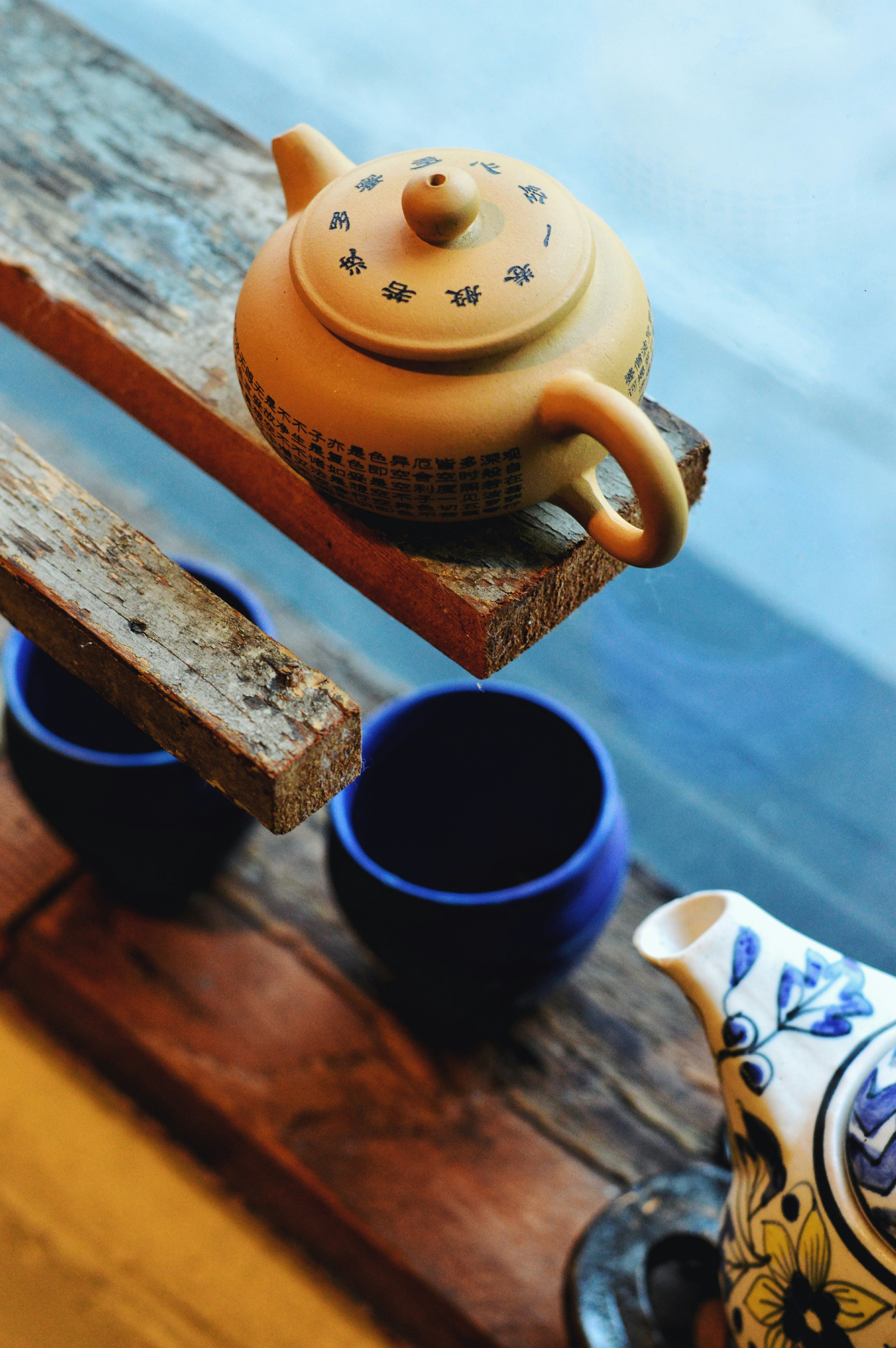 Ceramic Teapot on Weathered Wooden Planks Above Blue Cups